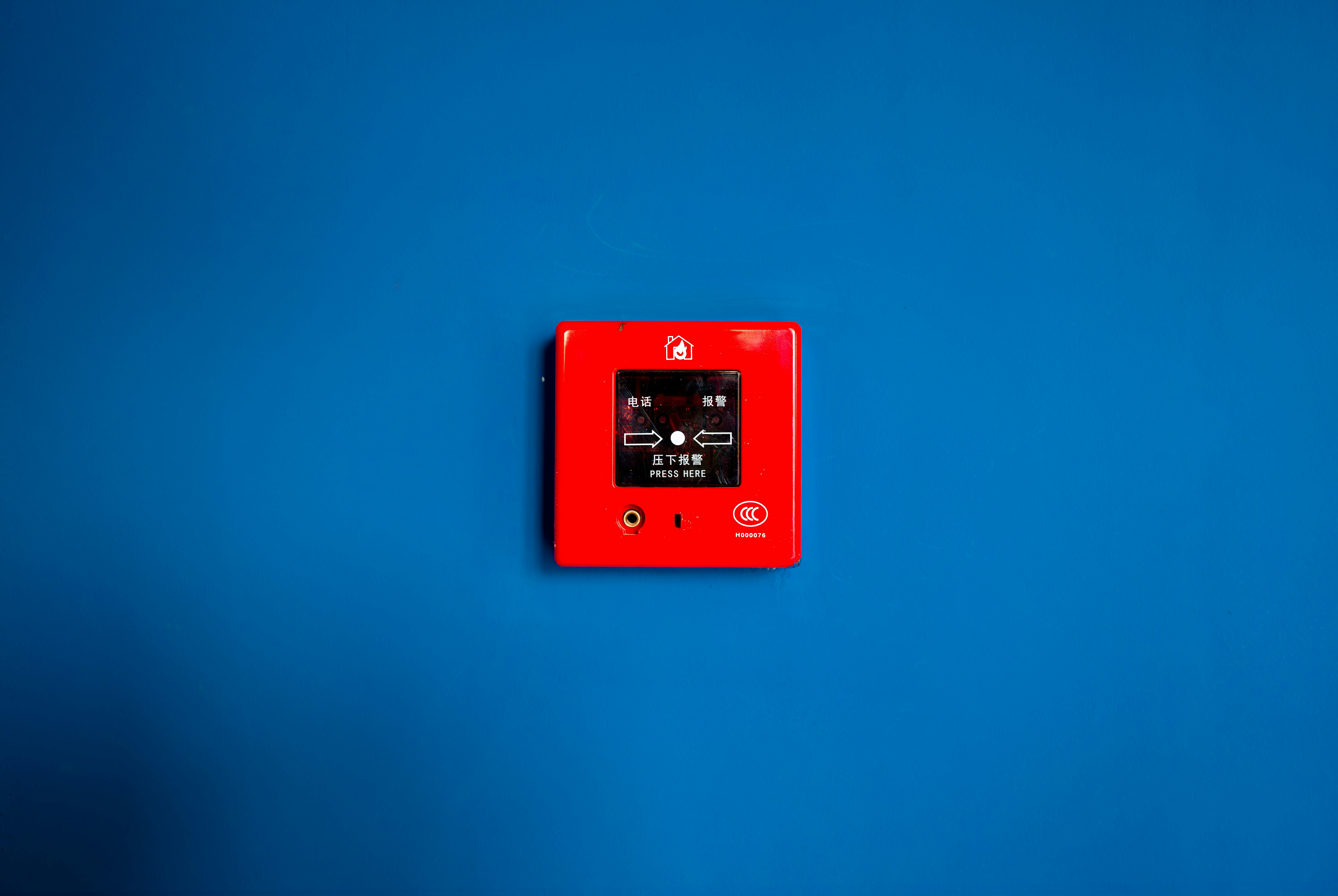 A vivid red safety device mounted on a solid blue wall, drawing focus through strong color contrast and minimalist composition.
