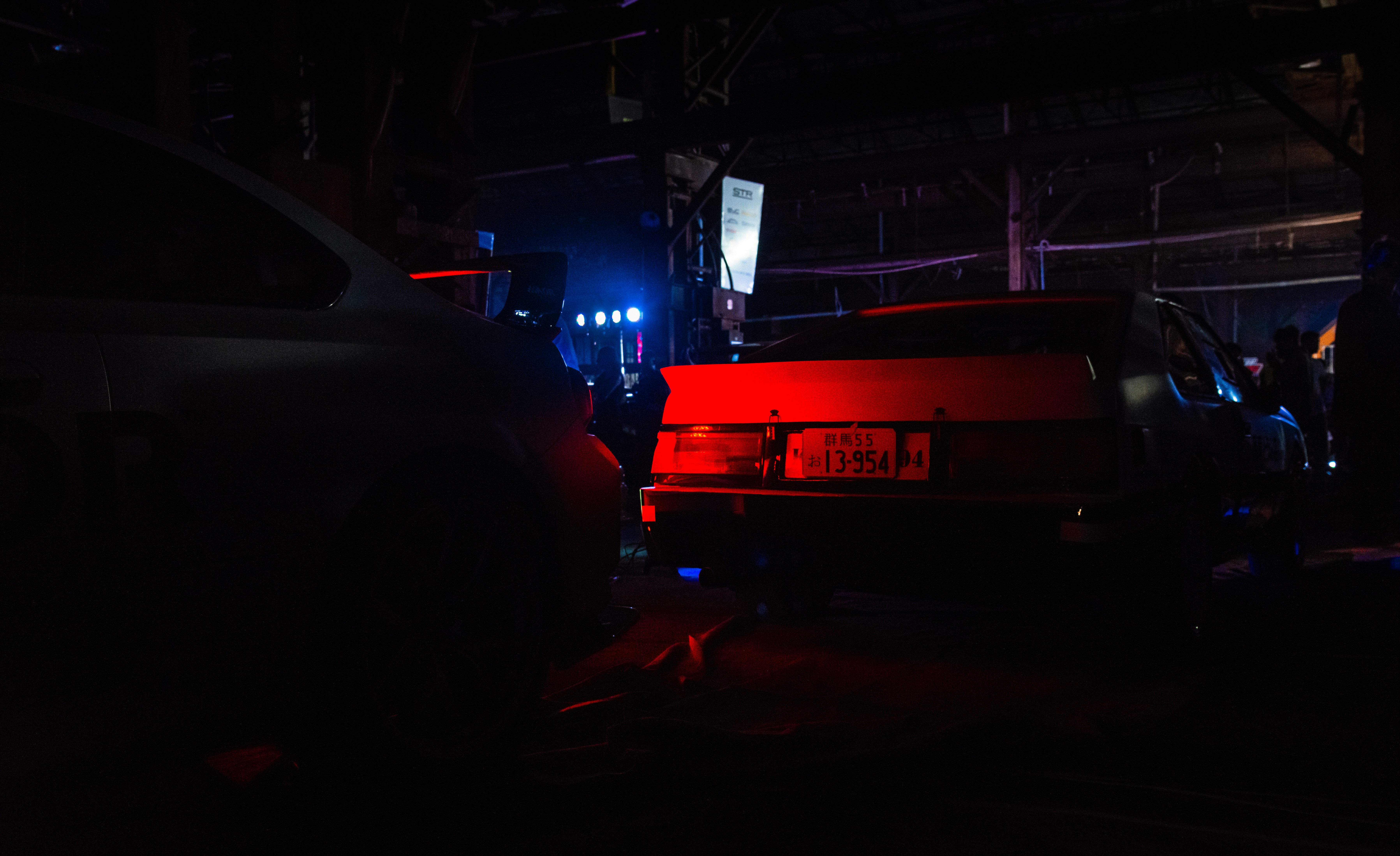 A white Toyota AE86 Corolla Levin inspired by the iconic Initial D racing car, displayed at an automotive exhibition inside the abandoned Richardson & Cruddas factory in Mumbai, India. Photographed at night with a red light flashing onto it. A special thank you to Khalid for letting me photograph his car (instagram.com/khalid.jdm).