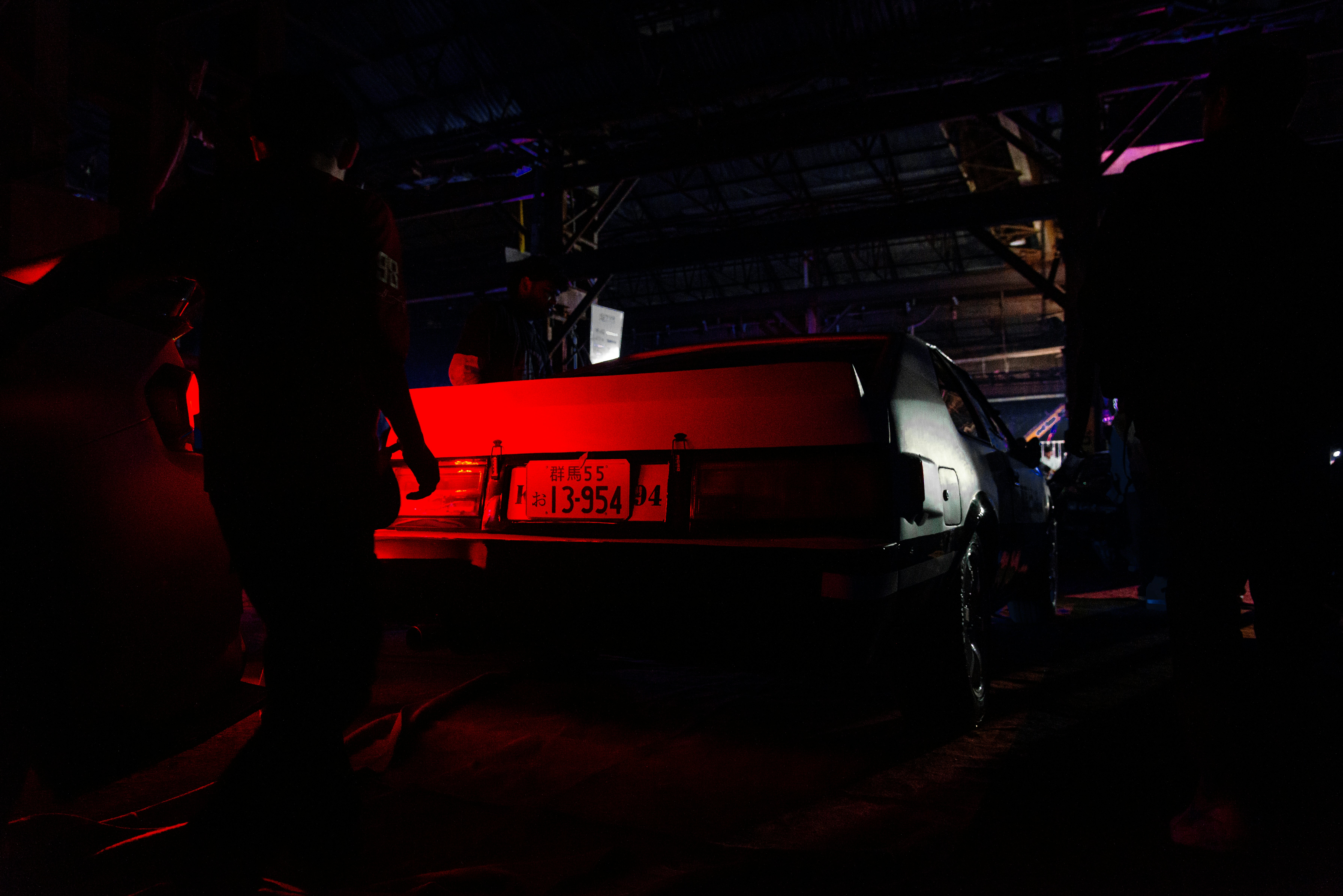 Midnight Garage: Red Tail Lights and Silent Figures