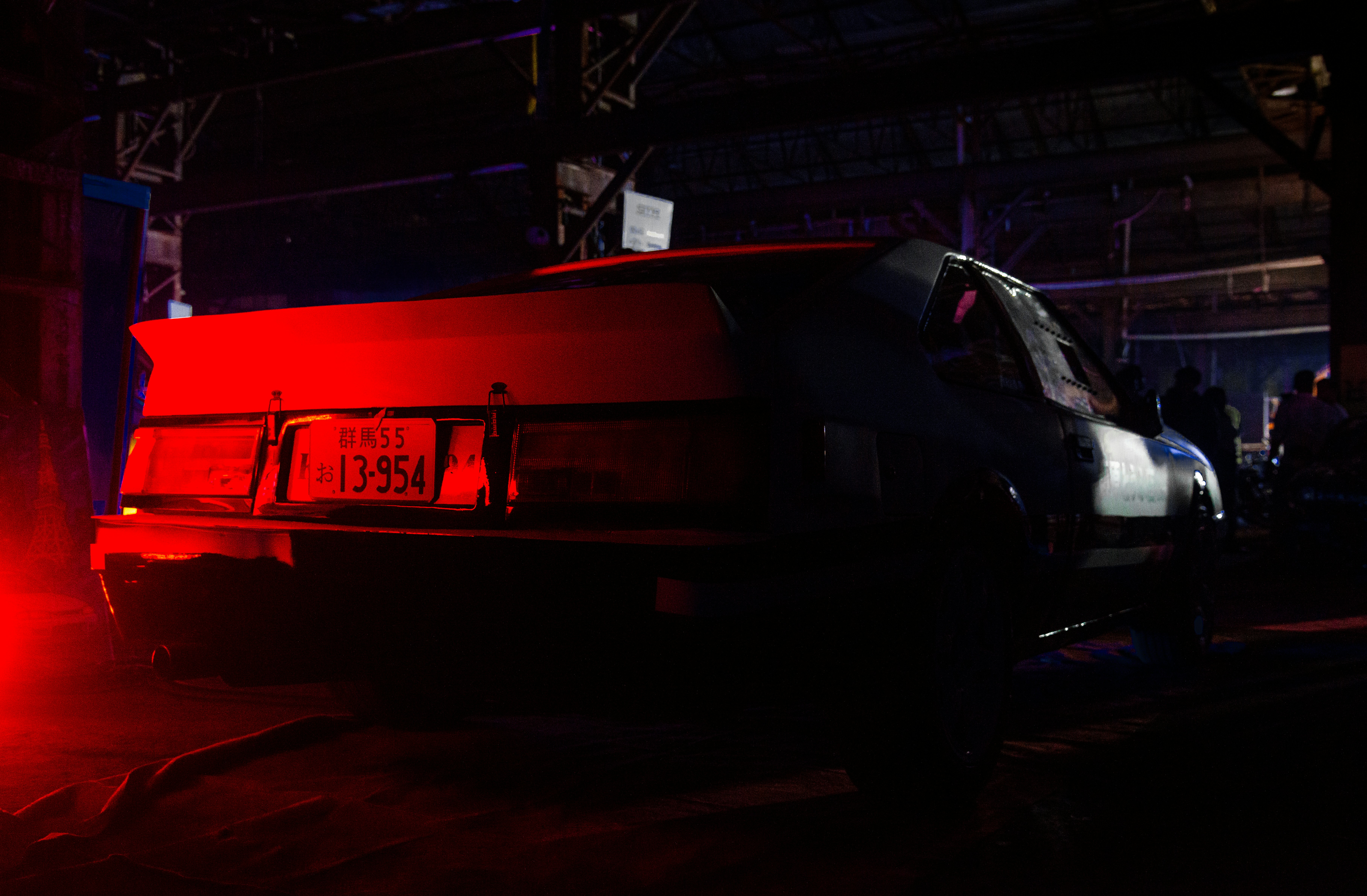 A white Toyota AE86 Corolla Levin inspired by the iconic Initial D racing car, displayed at an automotive exhibition inside the abandoned Richardson & Cruddas factory in Mumbai, India. Photographed at night with a red light flashing onto it. A special thank you to Khalid for letting me photograph his car (instagram.com/khalid.jdm).