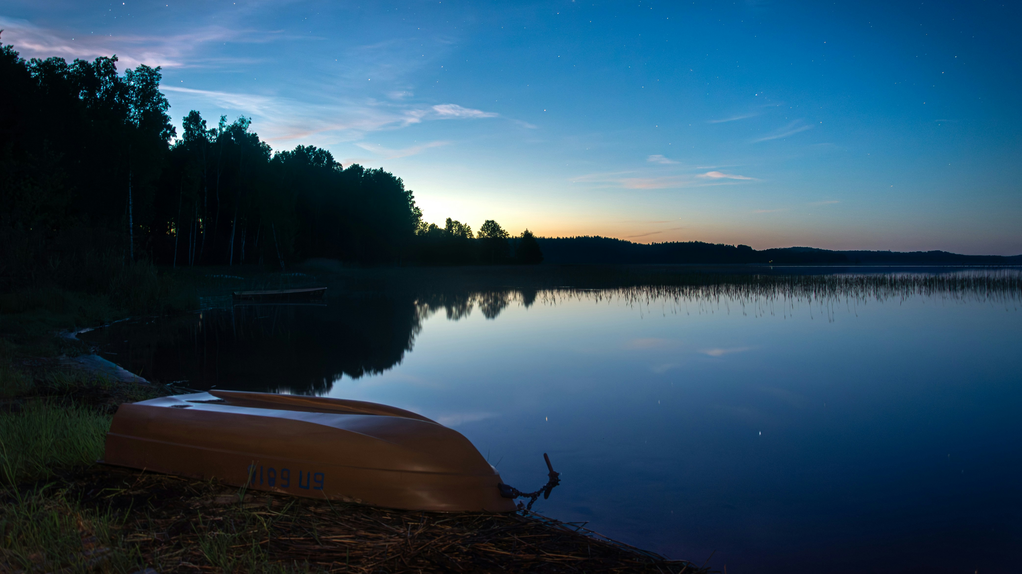 Low-light lakeside scene with a yellow canoe resting on the shore and a glassy water mirror reflecting trees and the twilight sky.