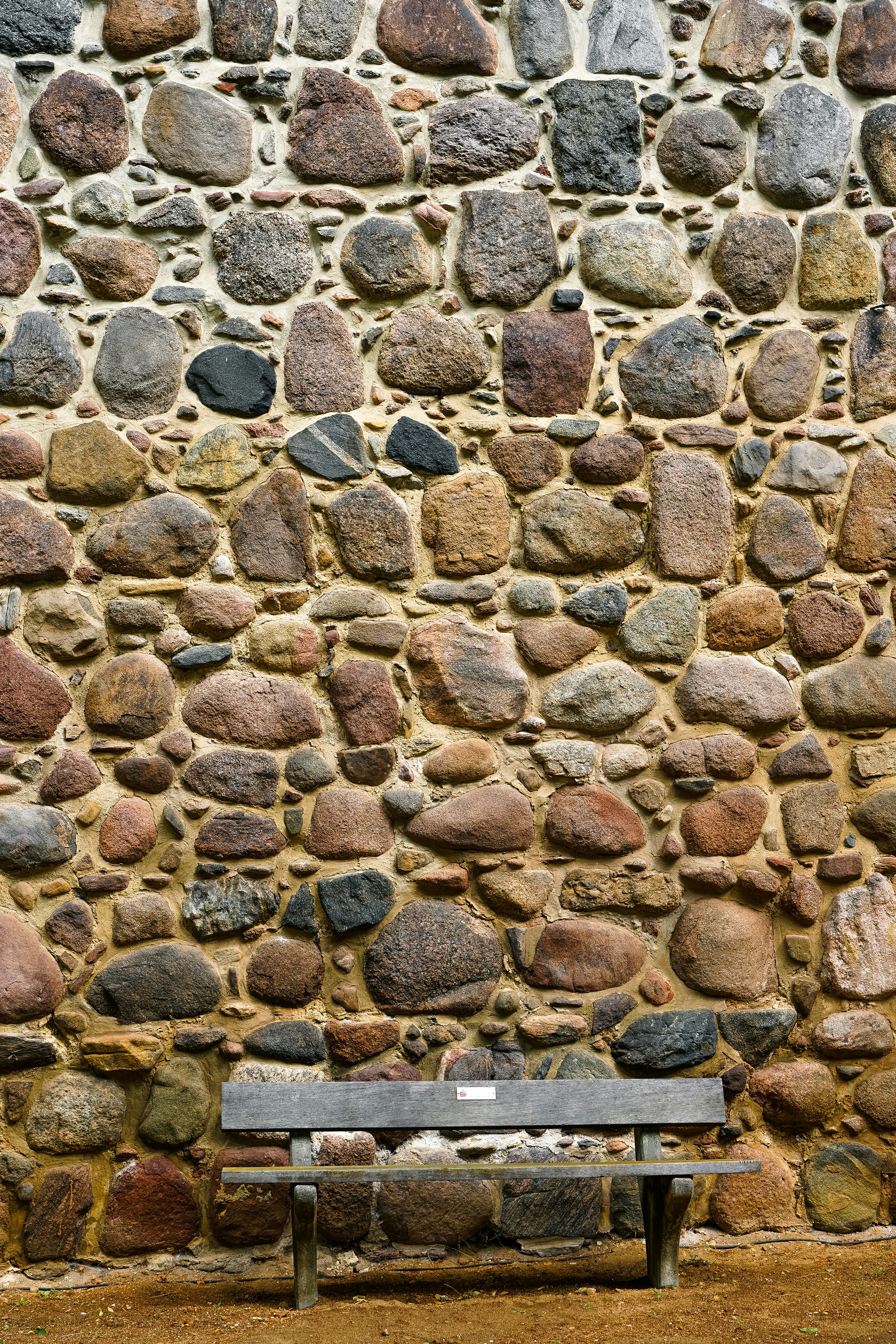 Stone Wall Serenade: A Quiet Bench Beneath Weathered Pebbles