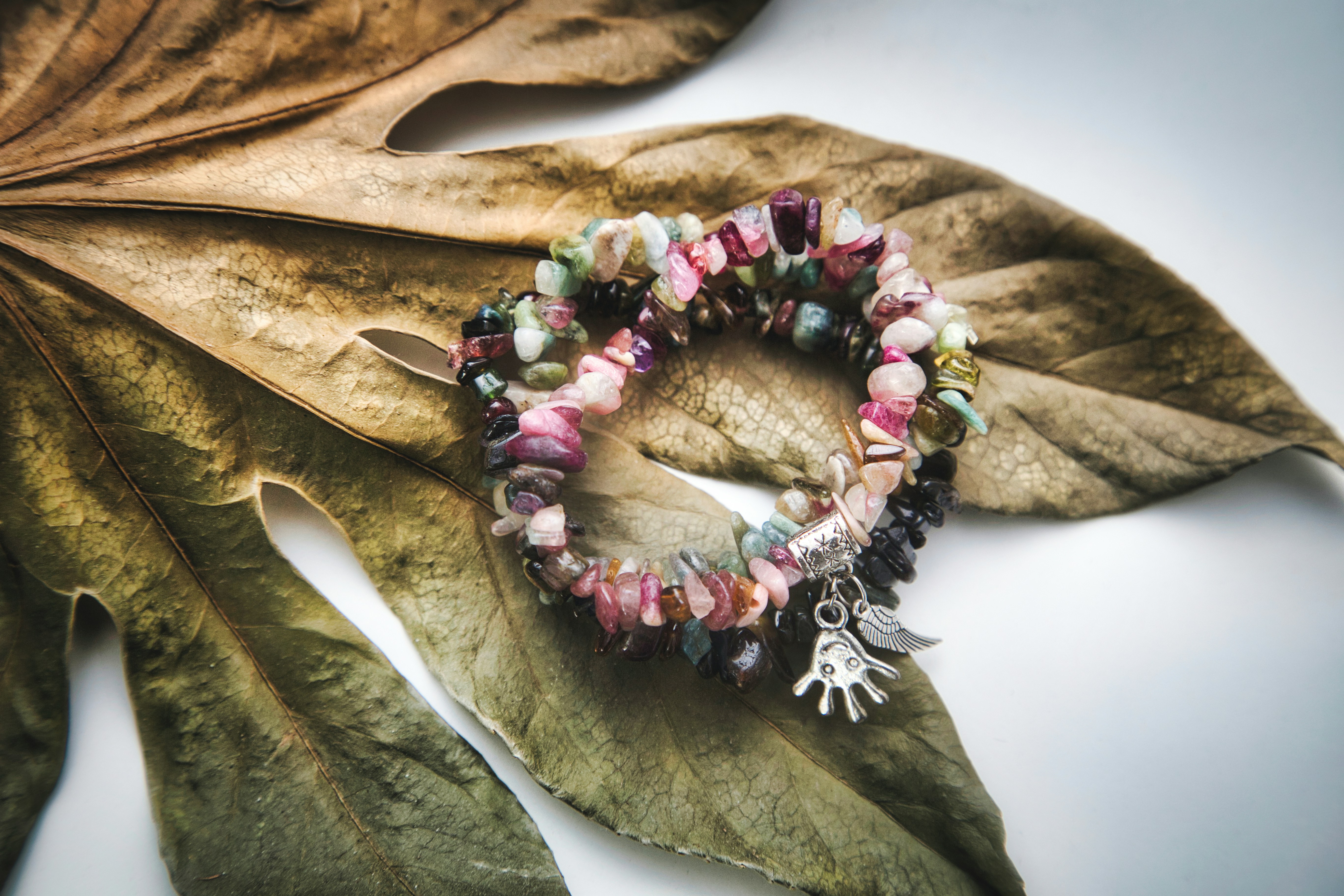 Colorful stone bracelet laid atop a dried leaf, highlighted by soft fall light to emphasize texture and charm beads.
