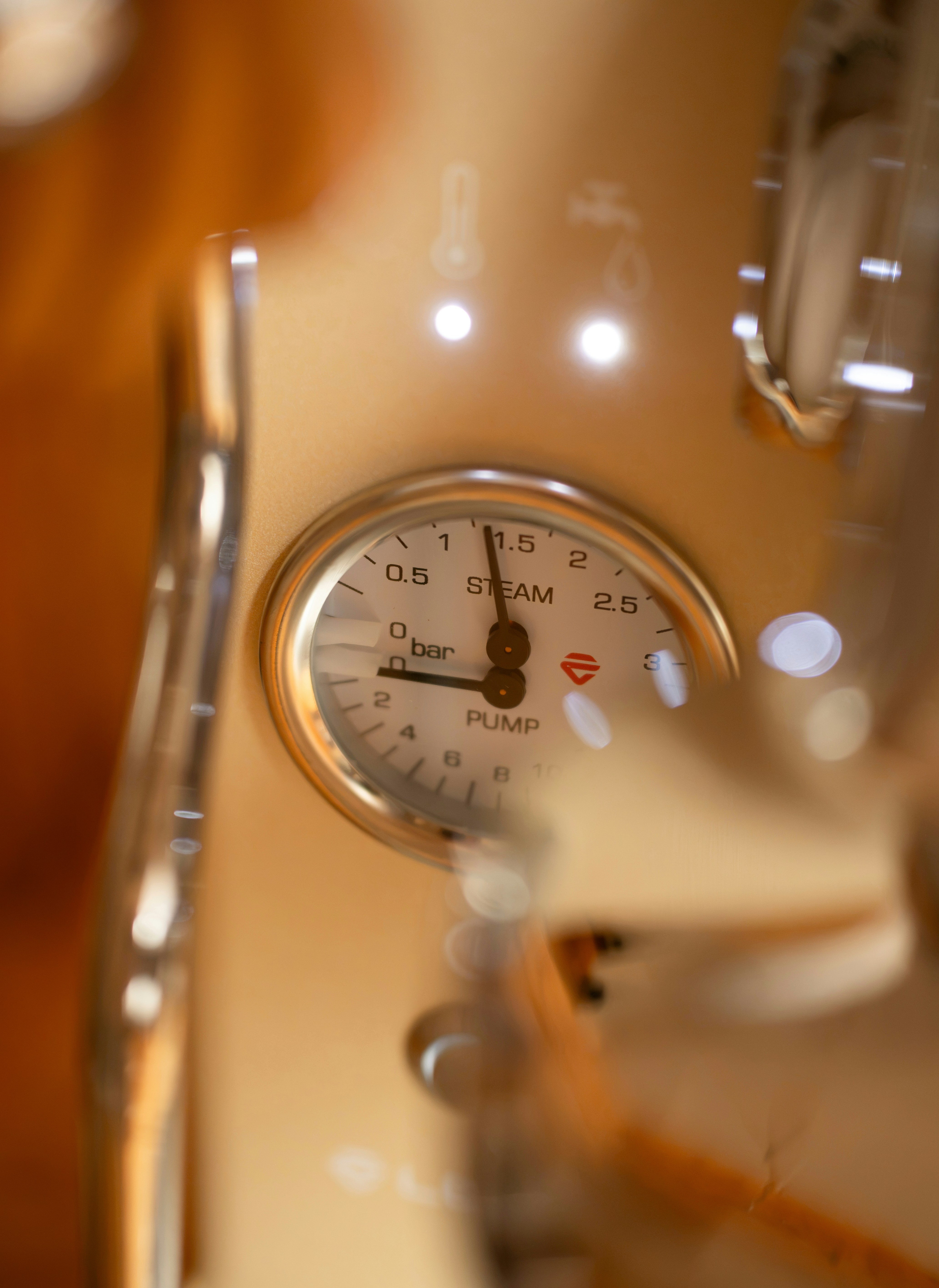 Close-up of a steam gauge on a vintage espresso machine bathed in warm copper glow