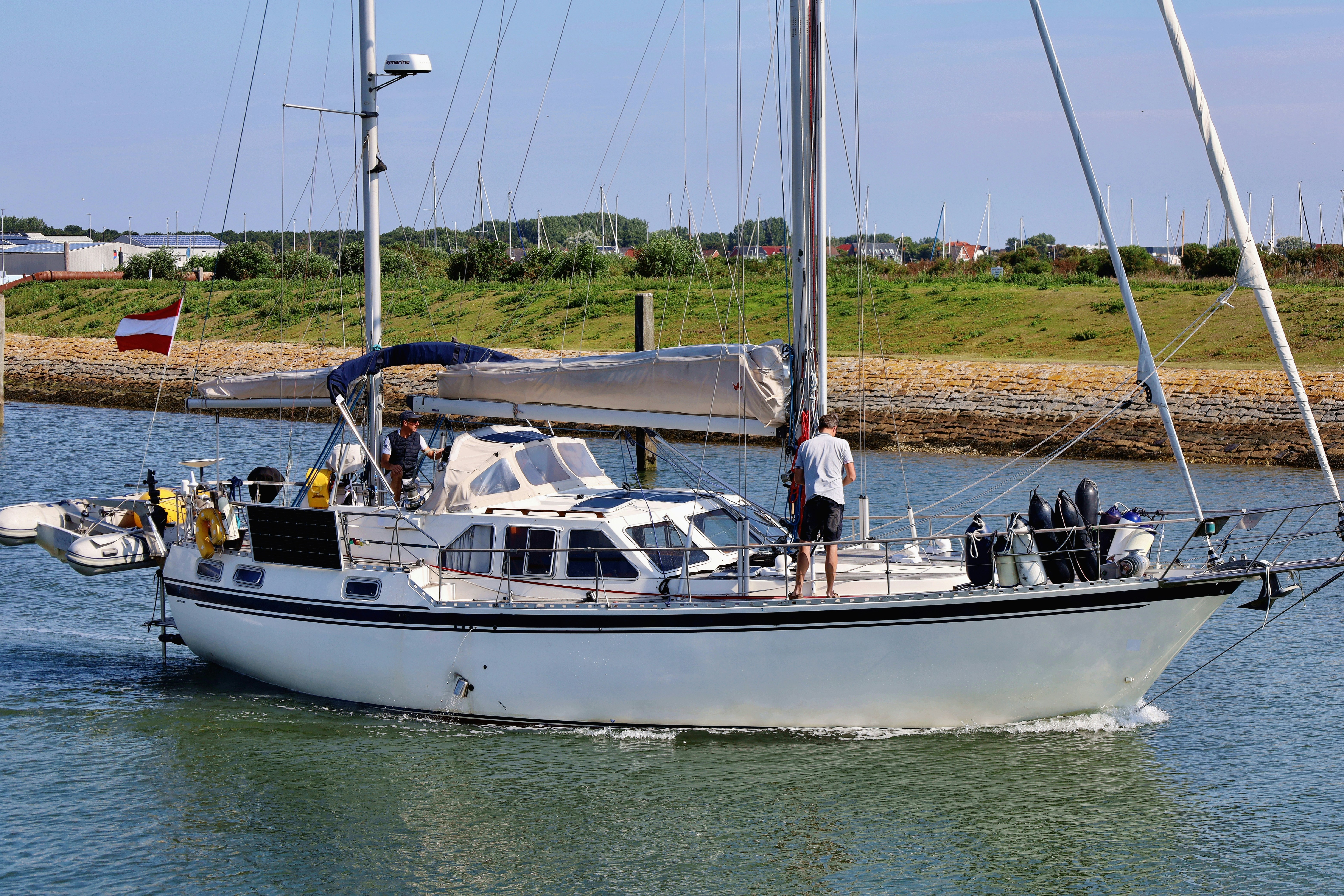 Sailboat in calm harbor: crew at the ready on a sunlit afternoon