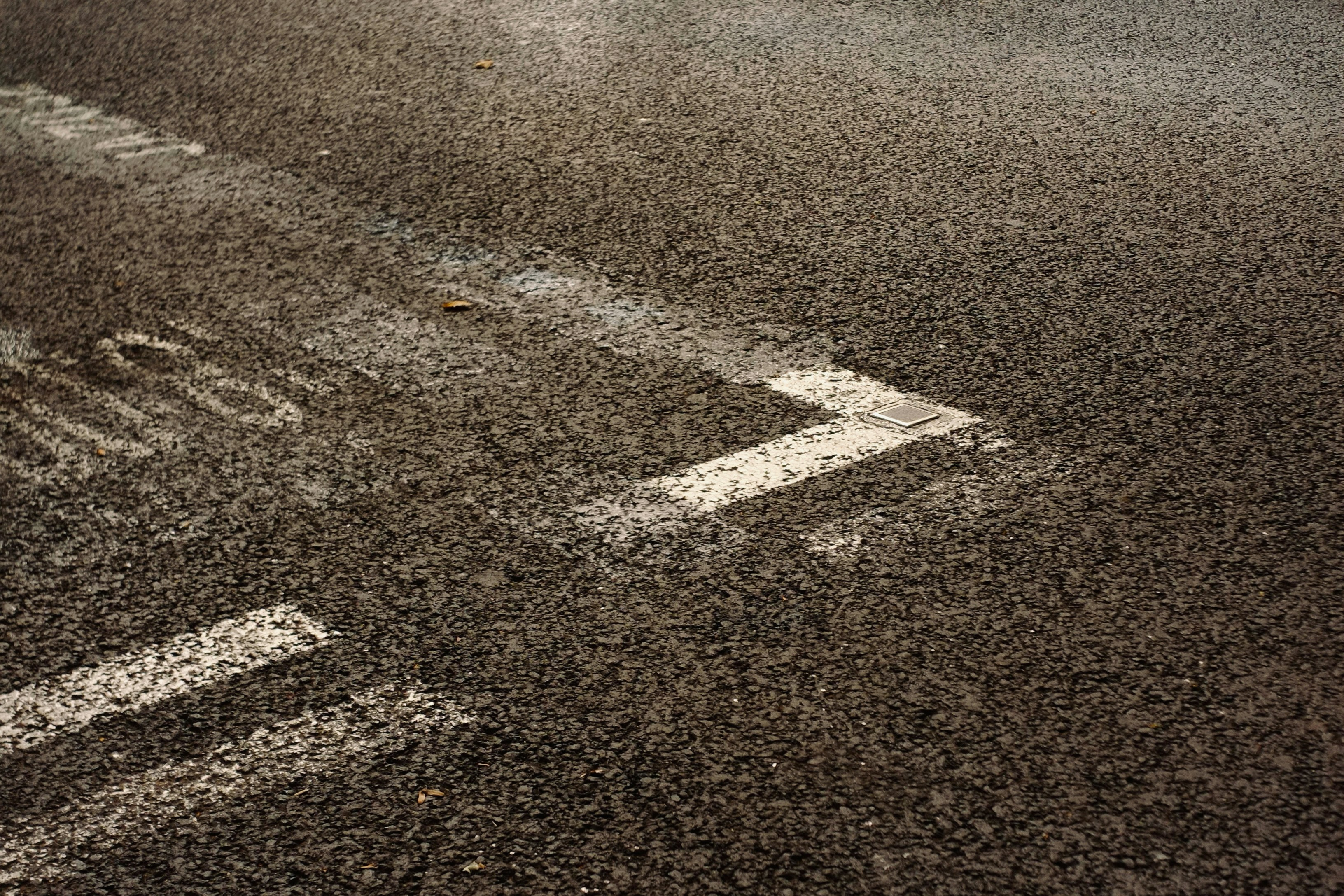 Discarded white road arrows and markings on rough asphalt surface, suggesting a parking or lane guidance area. The texture and wear convey a gritty, urban street scene.
