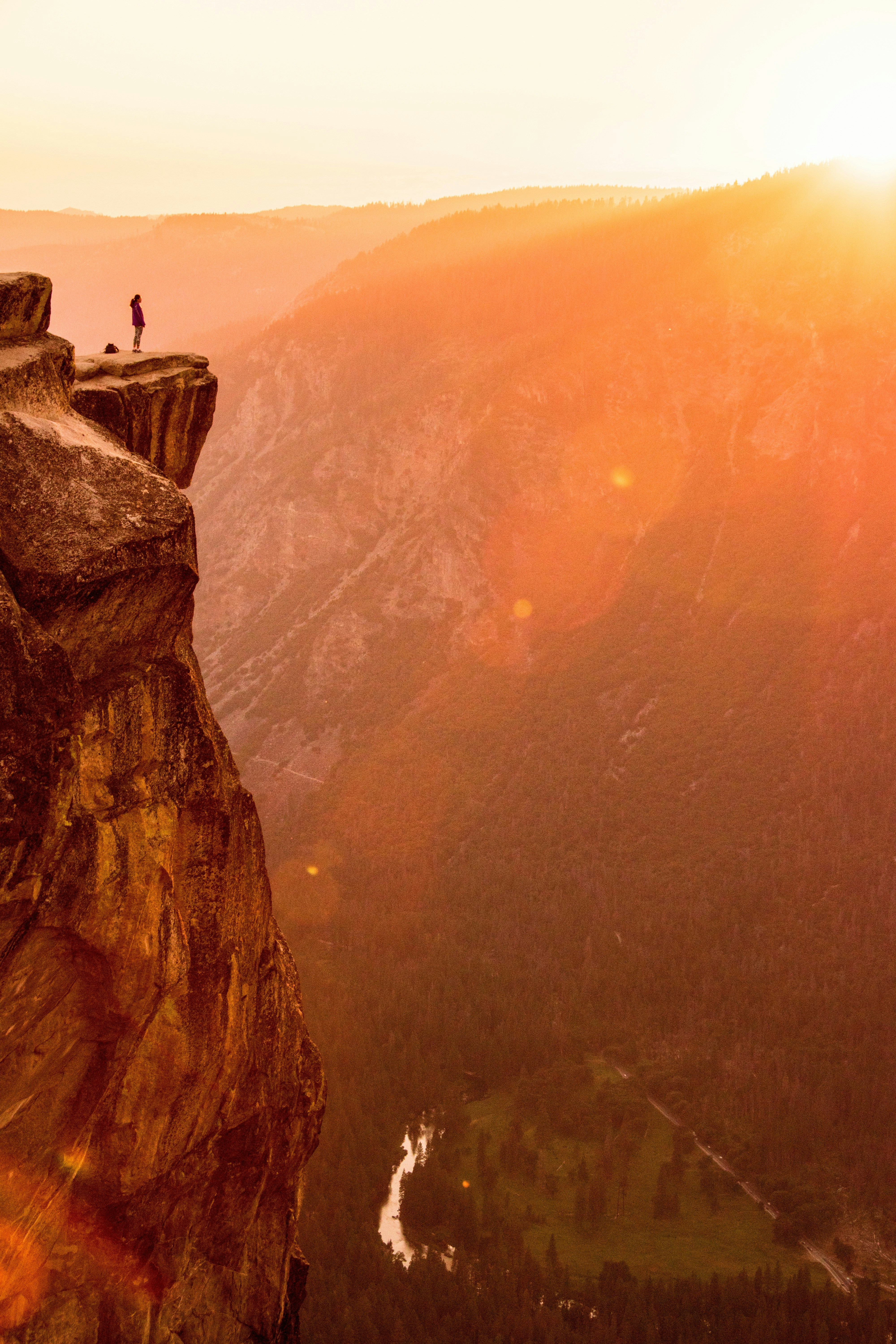 Edge at Dawn: A Lone Figure on a Cliff Veiled in Orange Mist