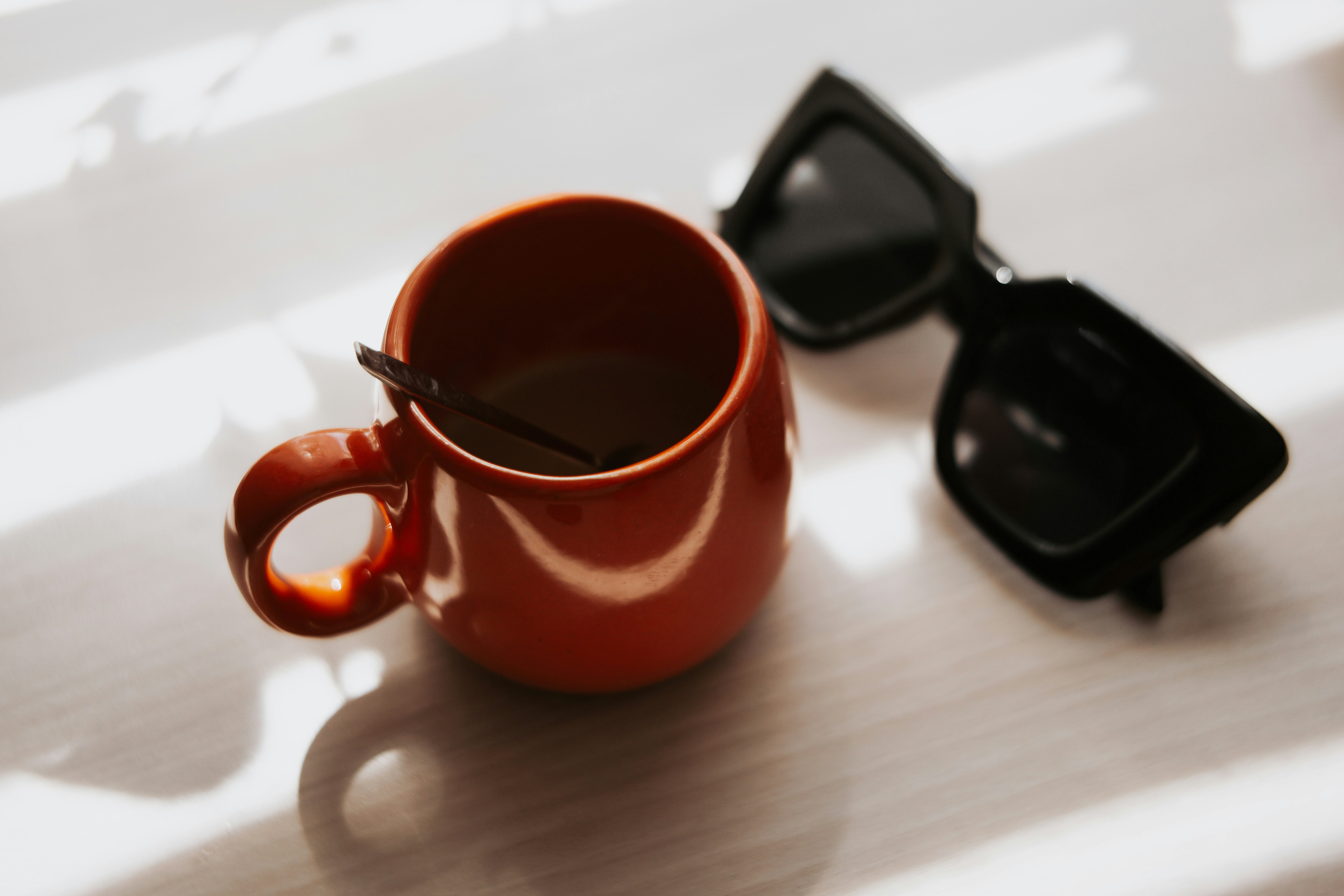 Warm Brew, Cool Shadows: A Red Mug and Sunglasses on a Sunlit Surface