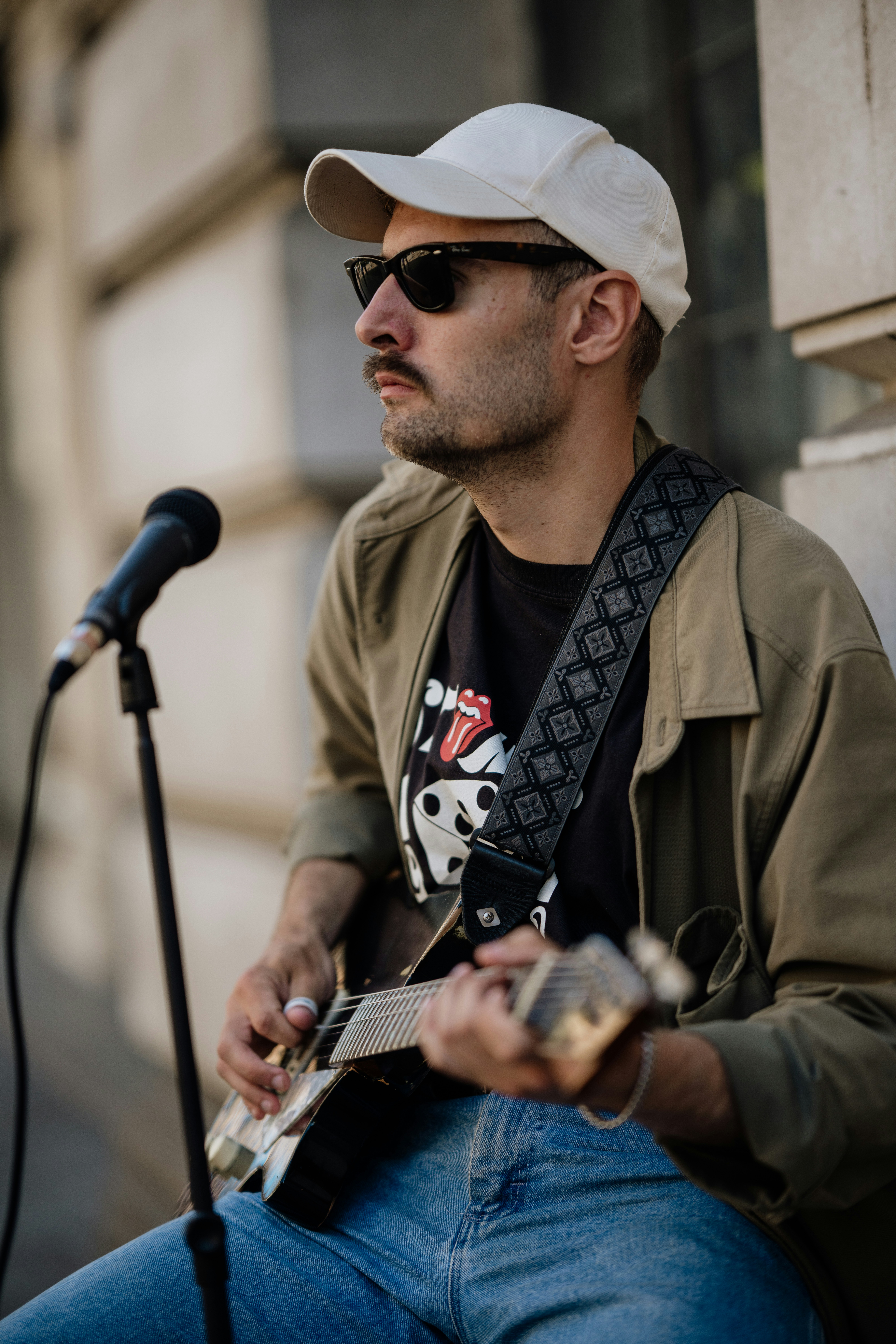 Street Serenade: A guitarist in cap and sunglasses plays softly beside a stone facade