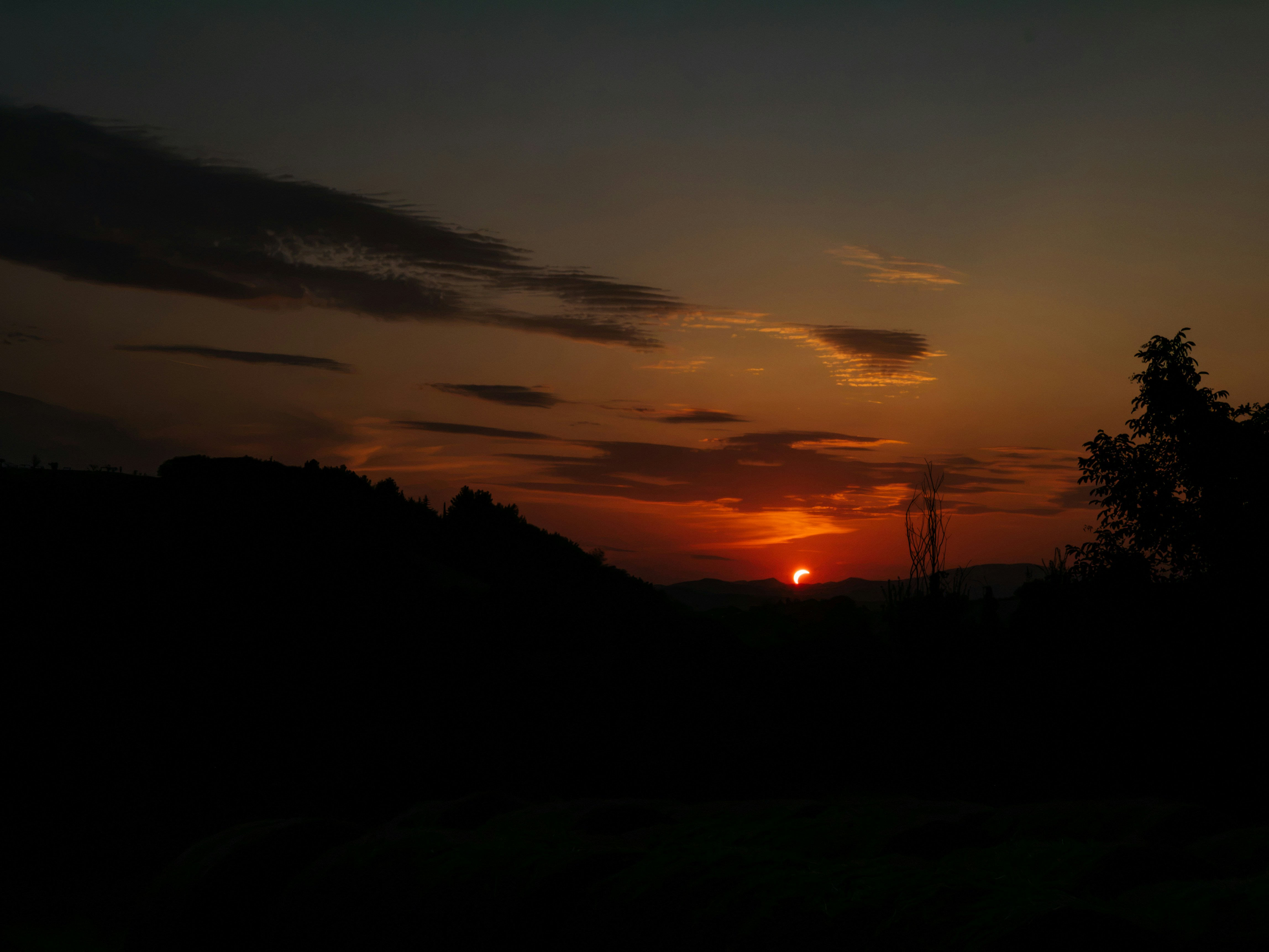 A partial solar eclipse over a dark silhouetted mountain range at low sun