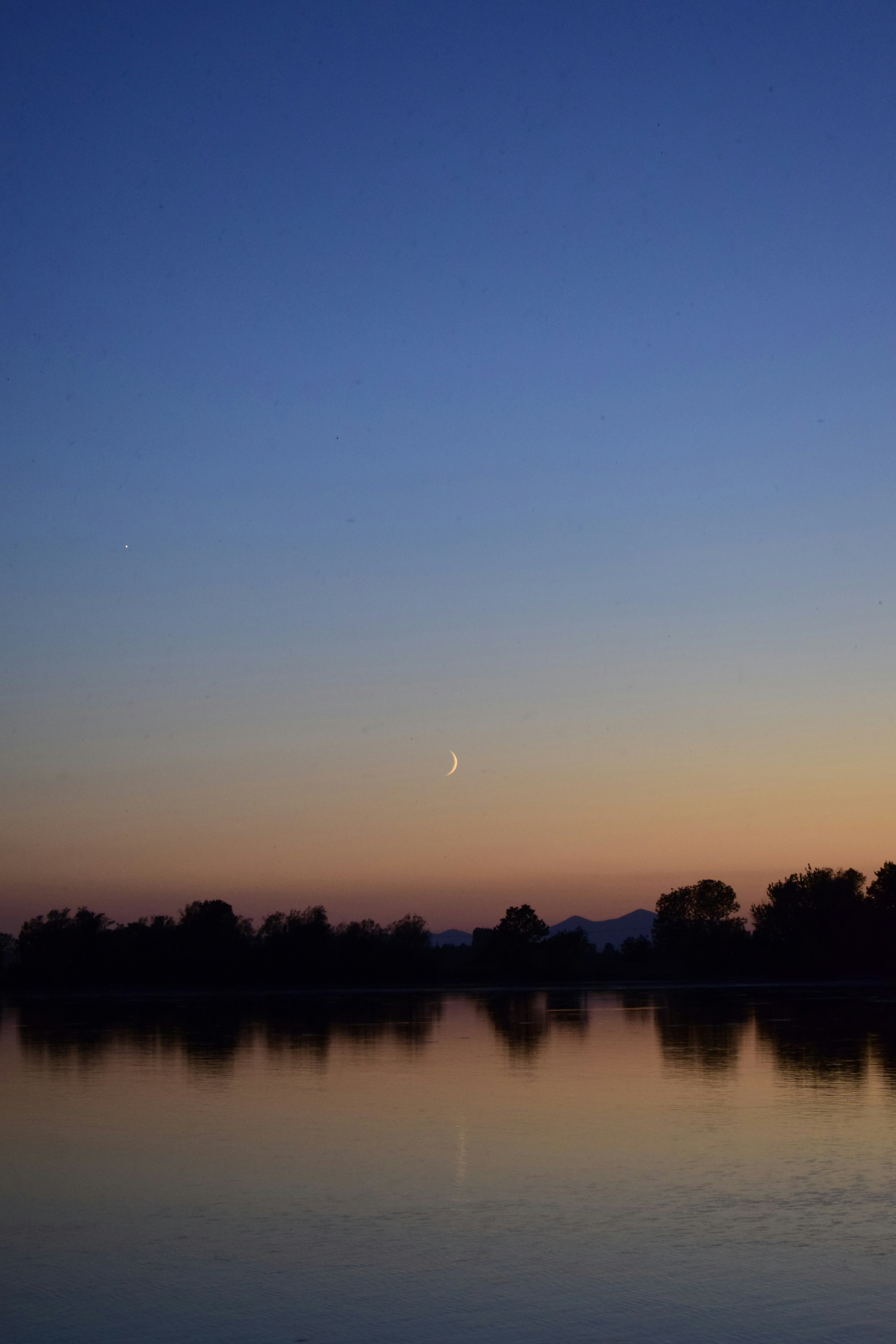 Dusk over the Quiet Lake: Crescent Moon Above Calm Waters