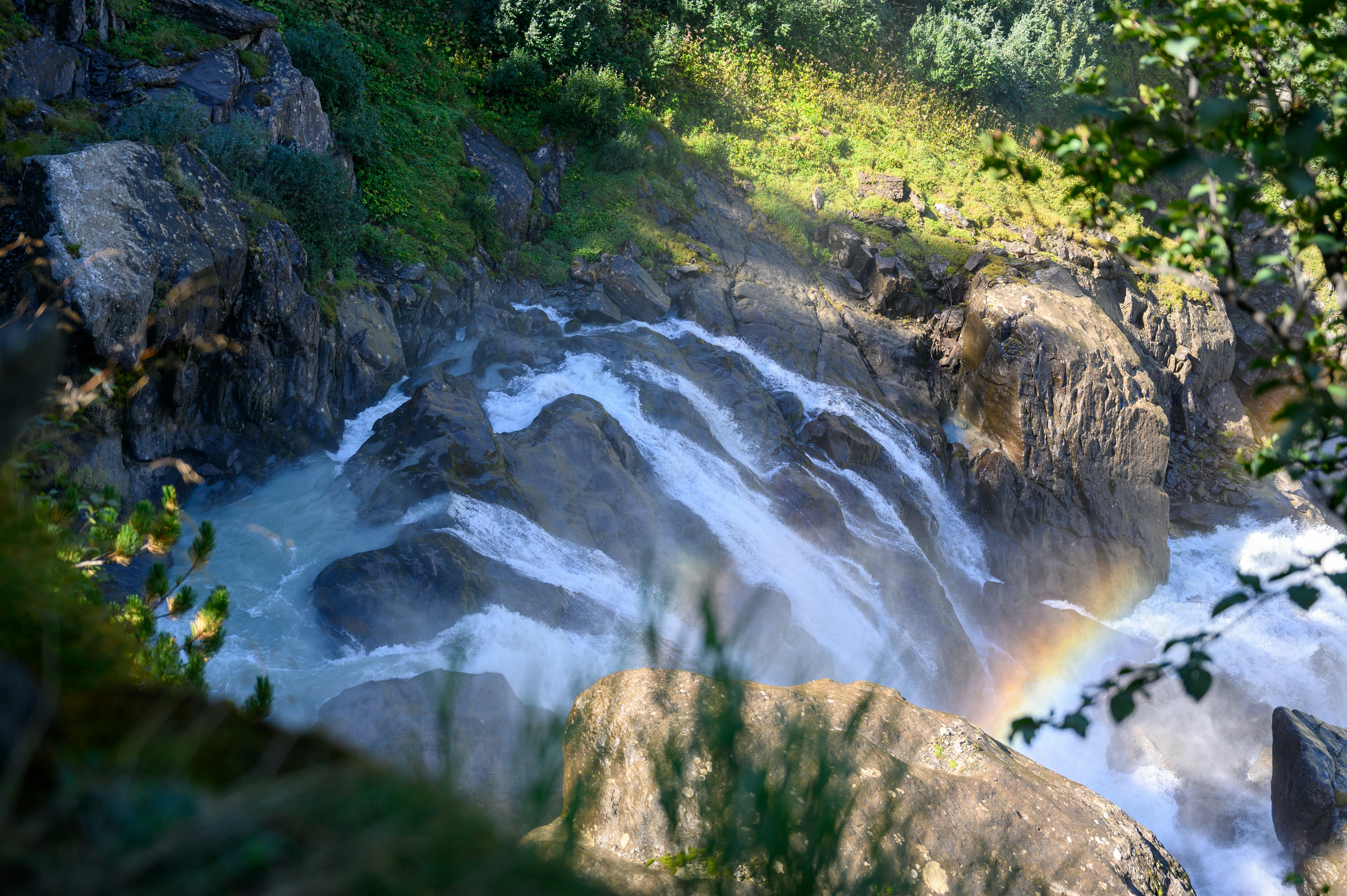 Mist-swept waterfall tumbling through rugged rocks captured from a forest vantage. A tranquil scene emphasizing motion and cool tones in a natural gorge.