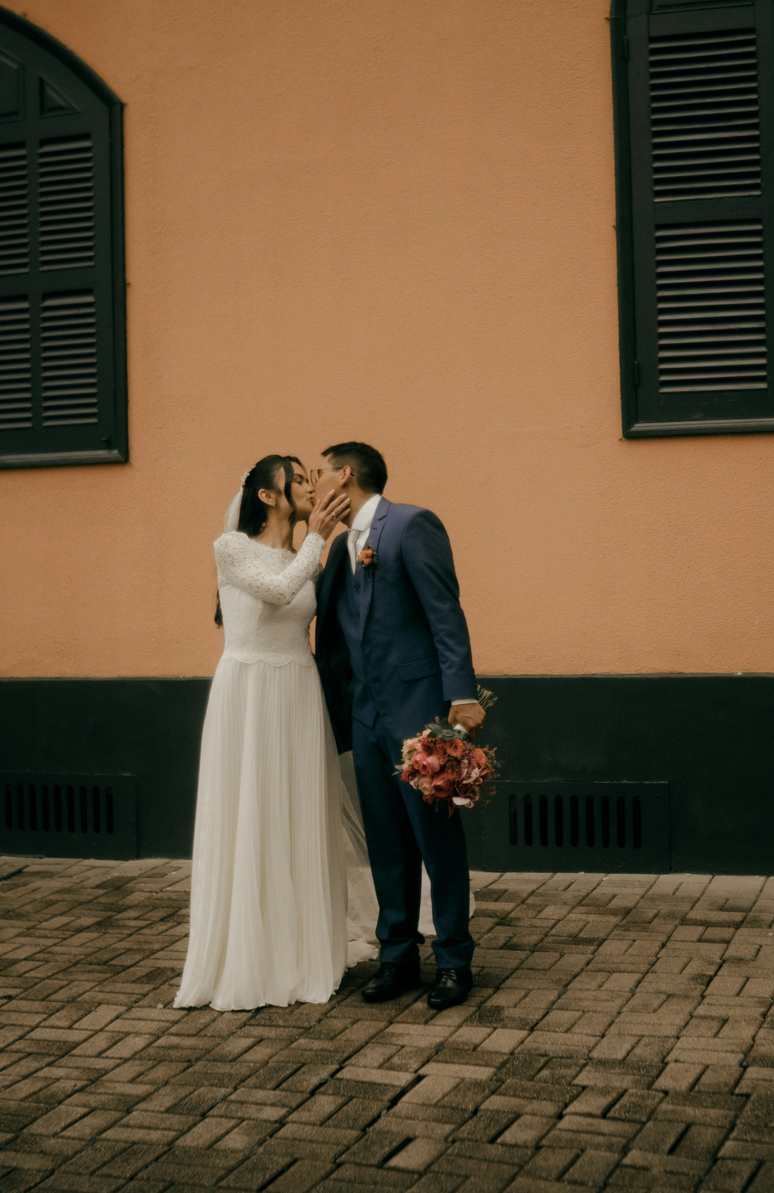 Veil and Vows: A Gentle Kiss Against a Peach Off-W-white Wall