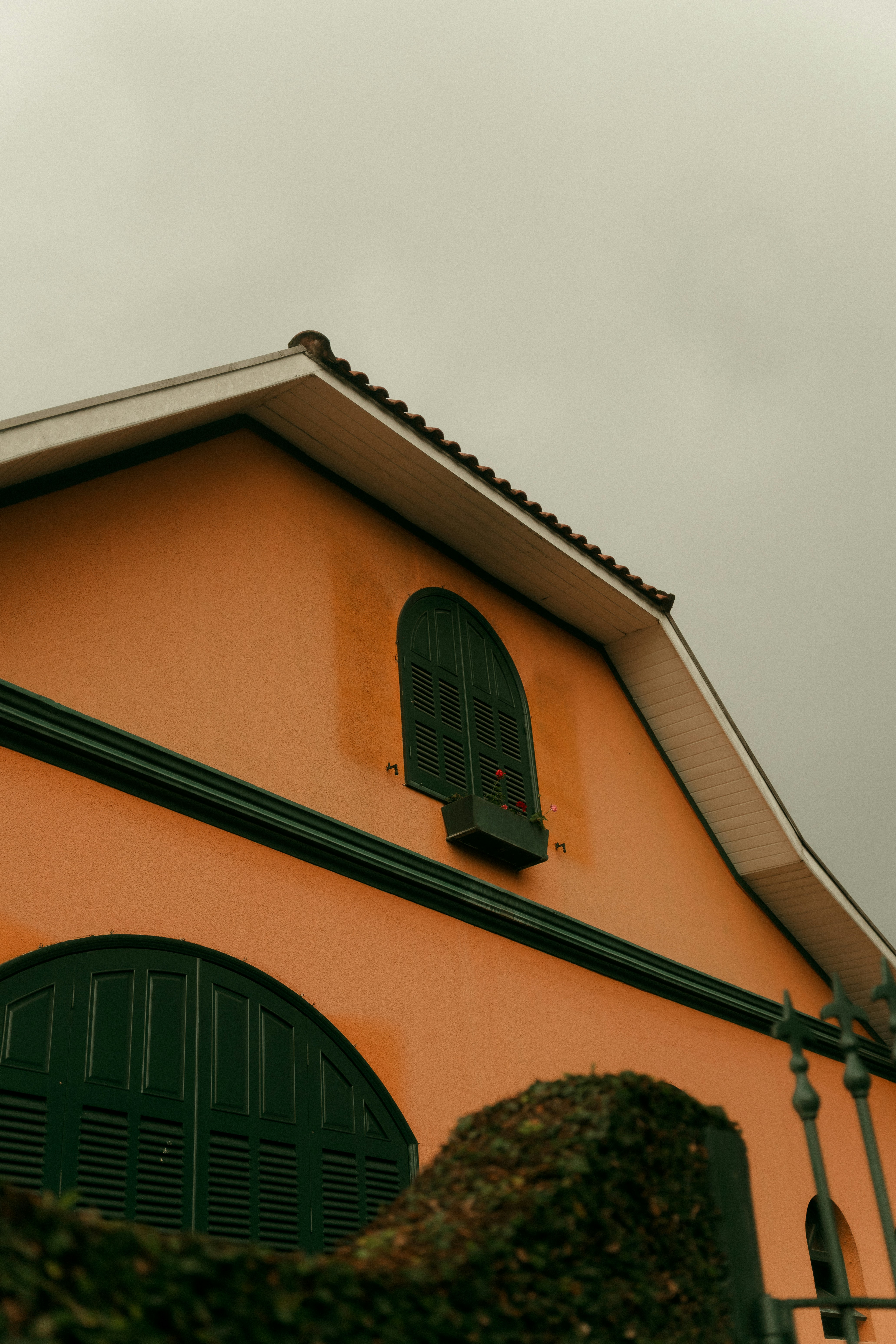 Terracotta Facade with Green Shuttered Window under an Oversized Roof