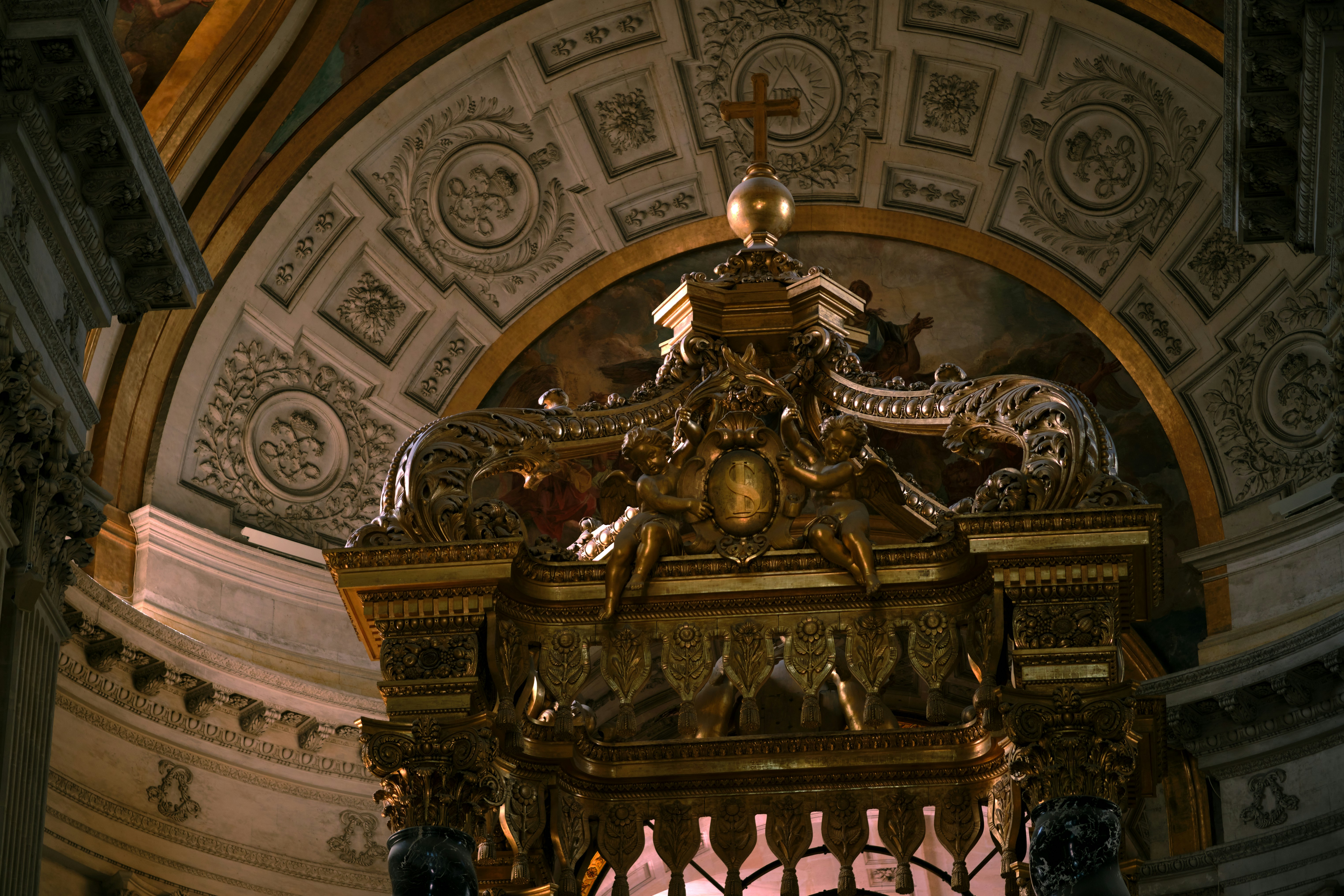 Intricate gilded canopy and organ loft rise above an ornate church interior, emphasizing sculpted details and architectural ornament in low light.
