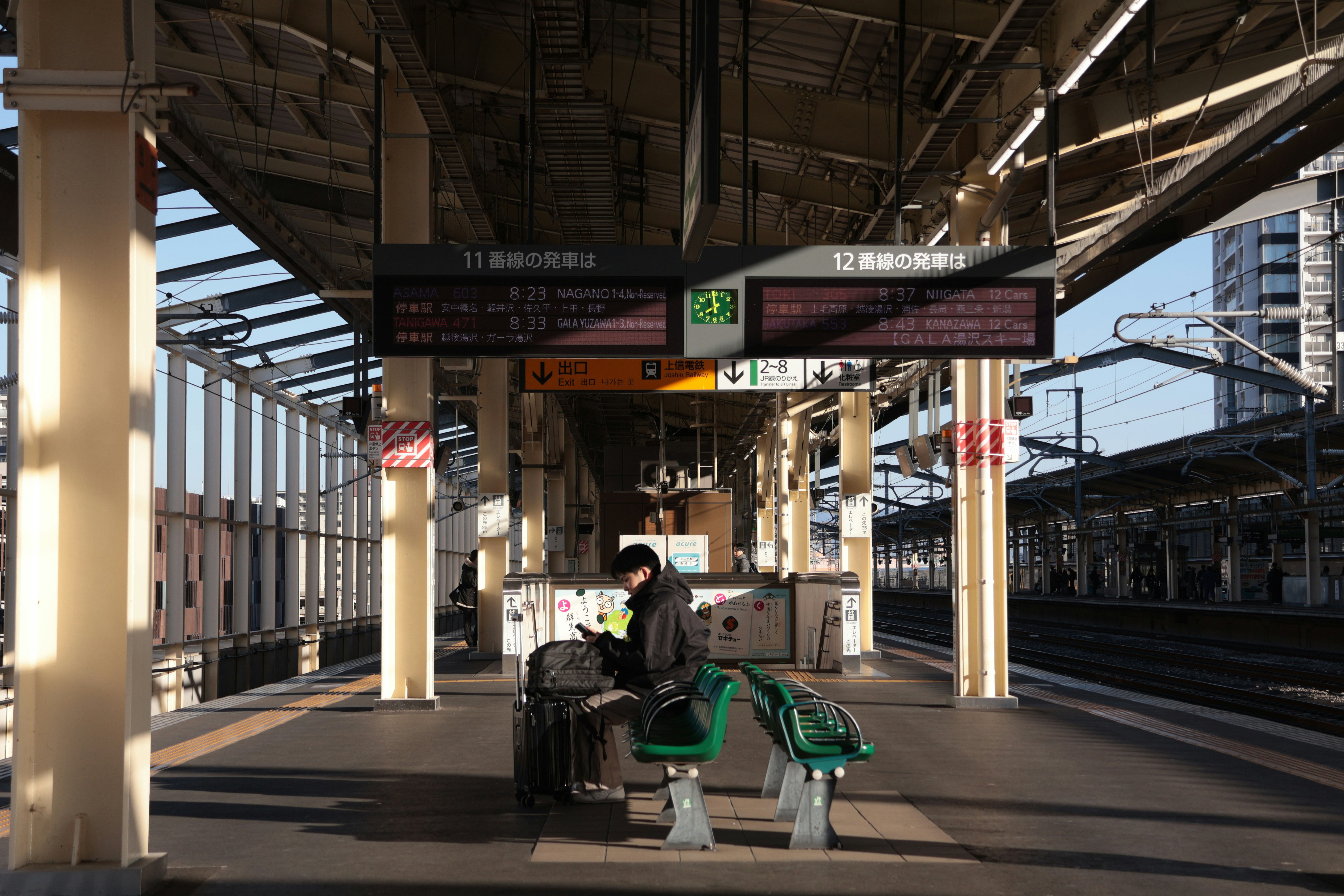 A person sitting on a green bench at a train station platform