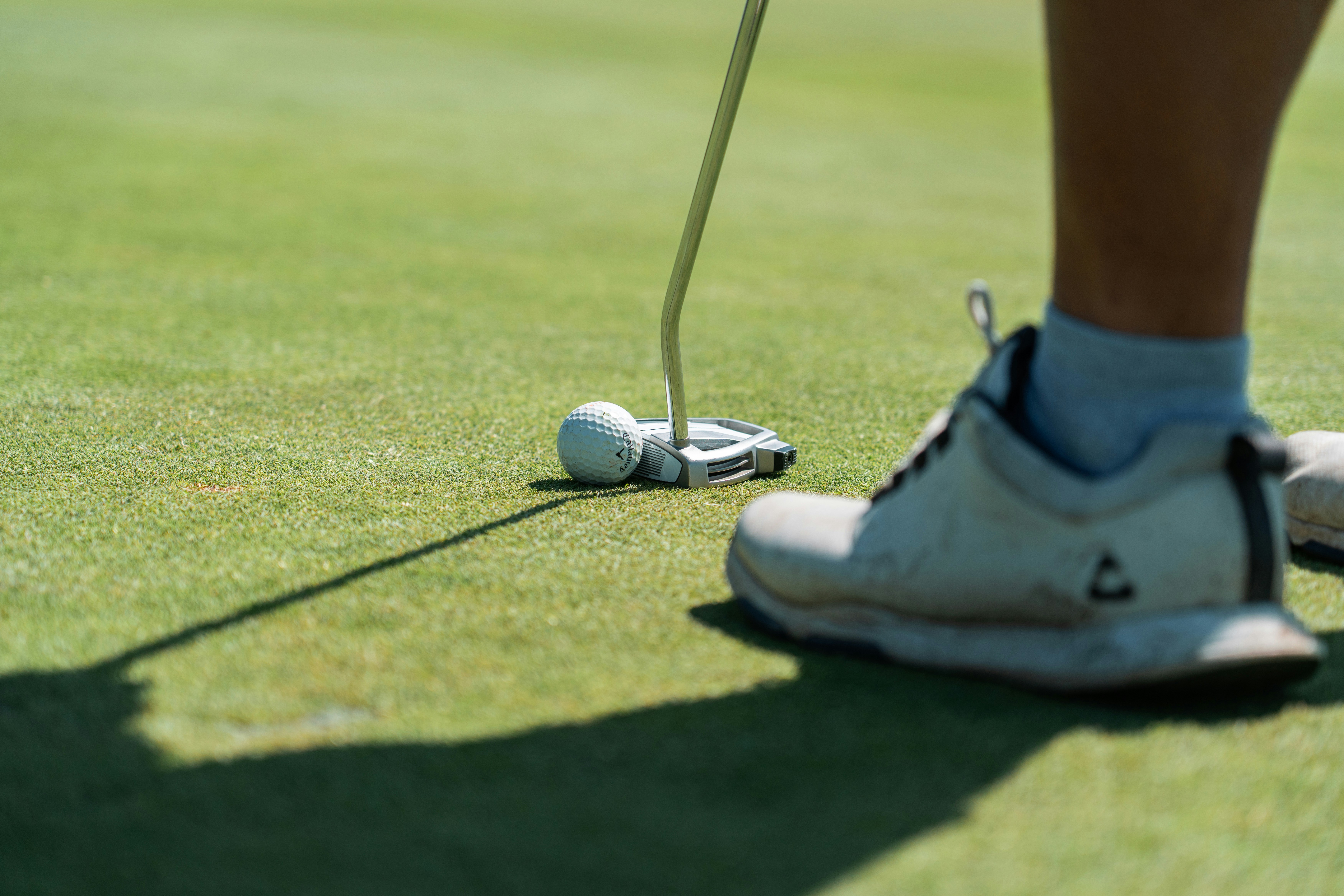 The Final Put: Ball, Club, and Footing on a Sunlit Green