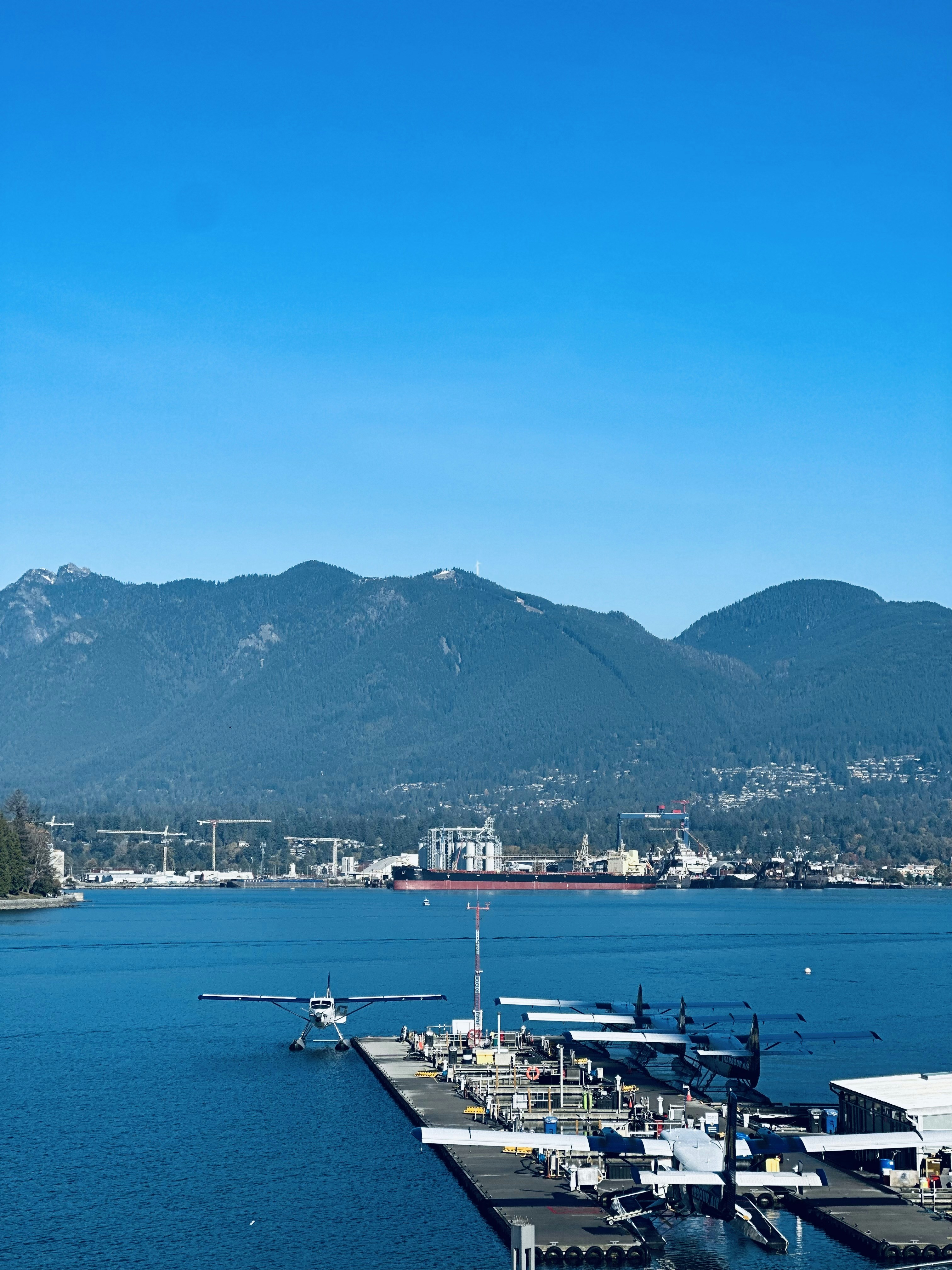 Blue harbor scene with a docked aircraft and distant mountains under a clear sky.