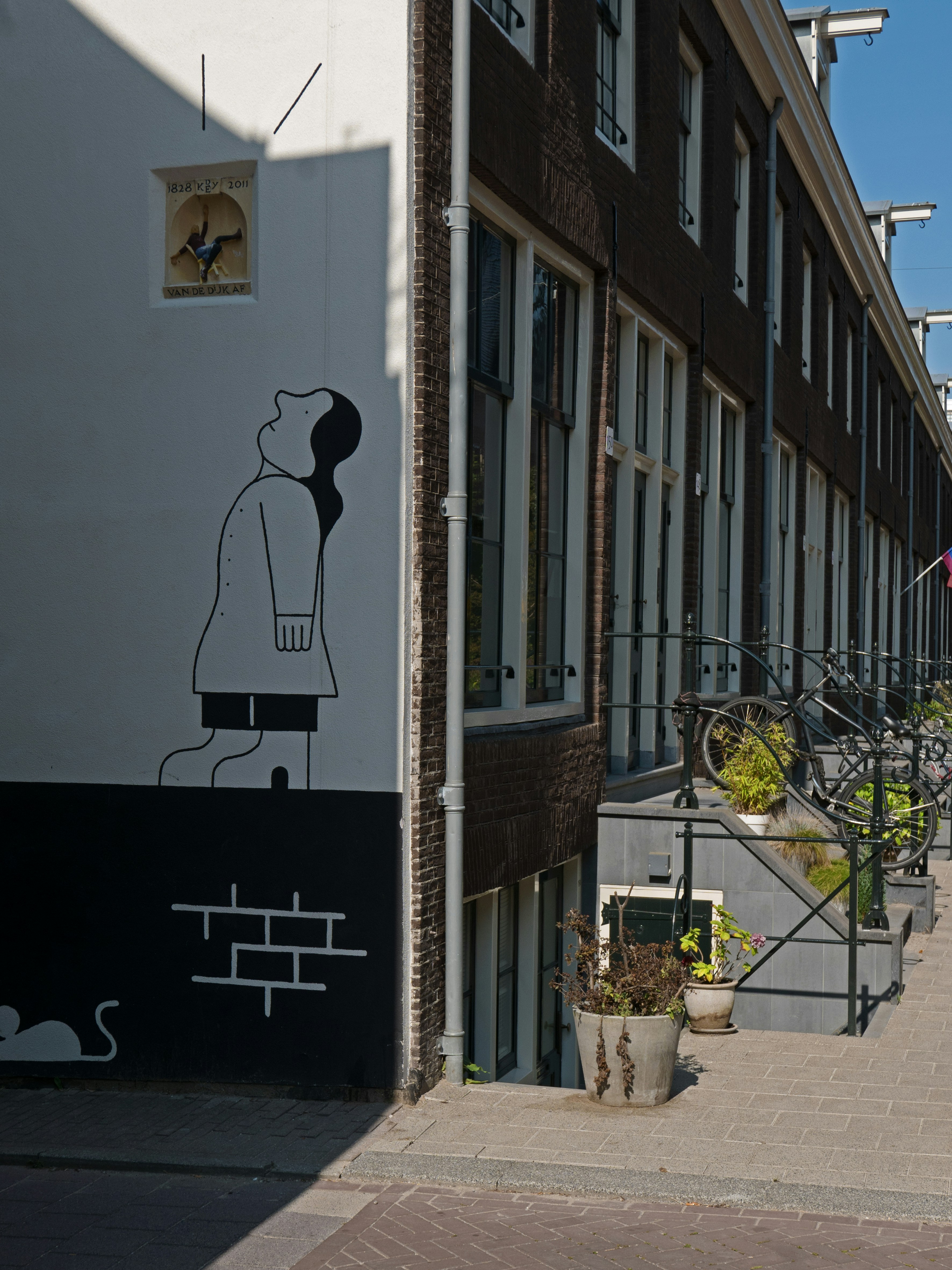 Photo of sunny street corner with a public art wall painting in Amsterdam old city; free images. // Foto van muurschildering op de straathoek van de Hoogte Kadijk in Amsterdam. Een man kijkt omhoog naar een oude gevelsteen met de hoge dijk; gratis afbeelding - straatfotografie Nederland in gratis download foto voor muur-poster en wallpaper.
