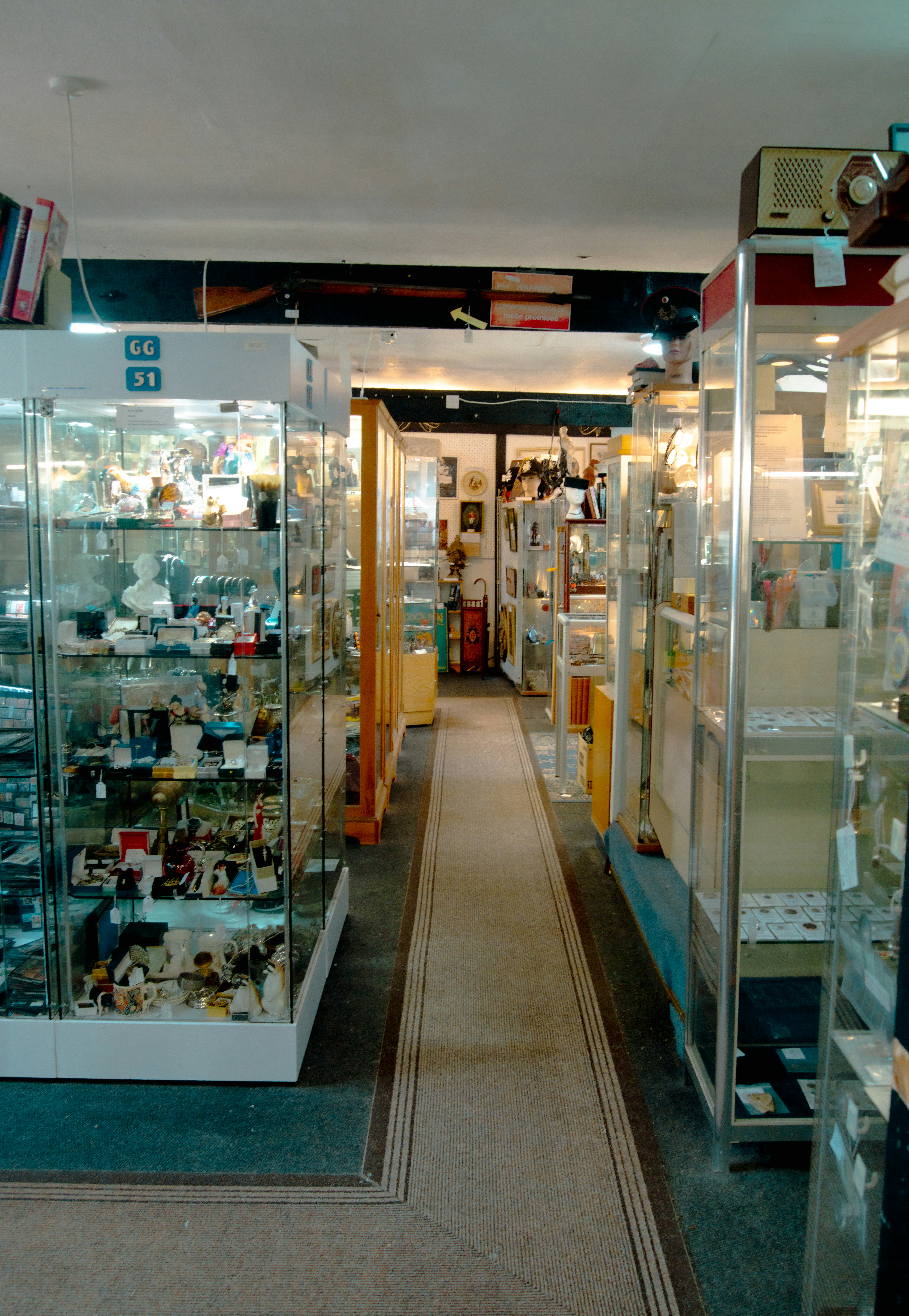 Long glass-display aisles line a vintage shop, filled with trinkets and collectibles under warm lighting.
