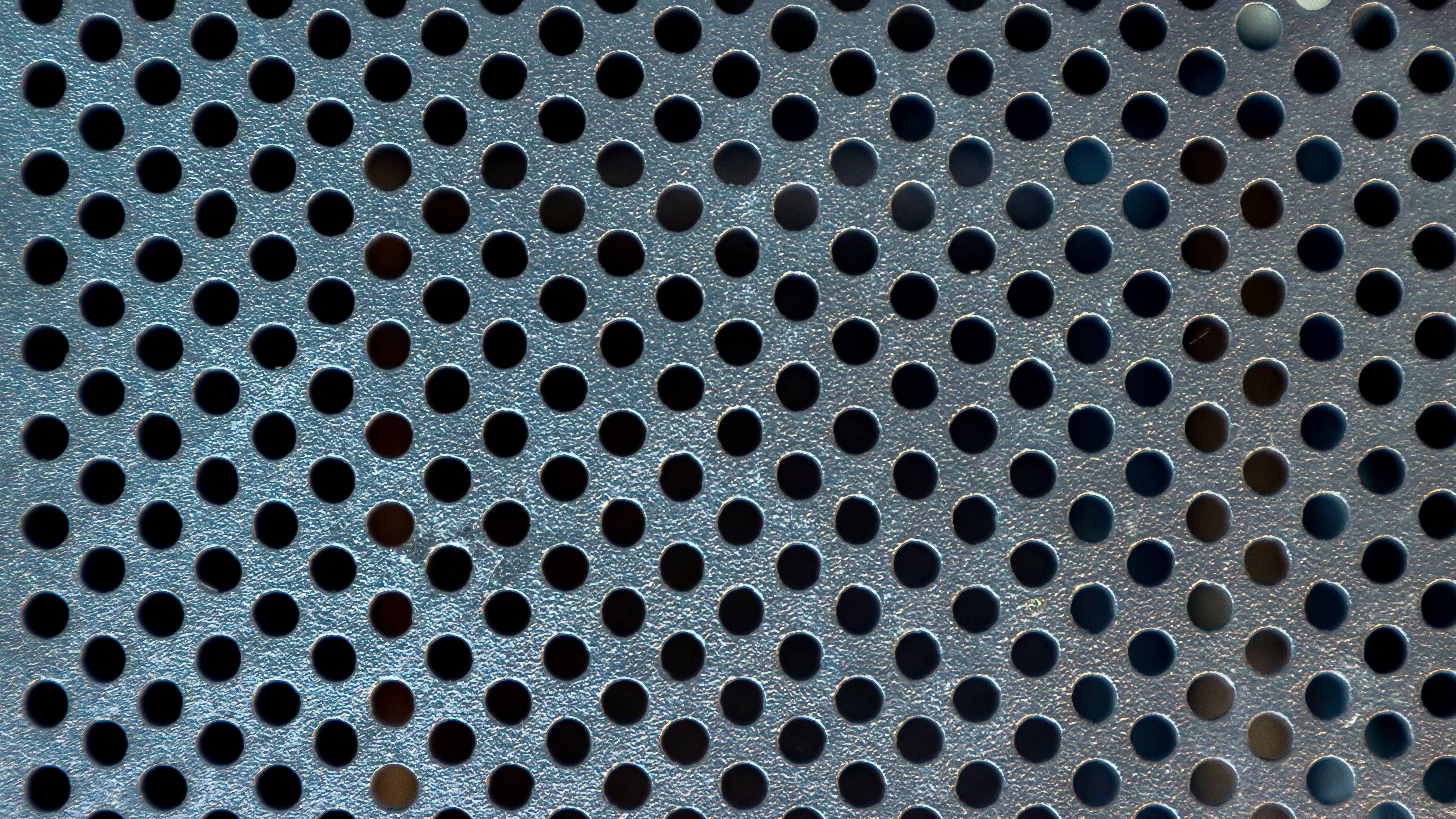 Close-up of a perforated metal surface with evenly spaced circular holes creating a repeating pattern and subtle reflections.