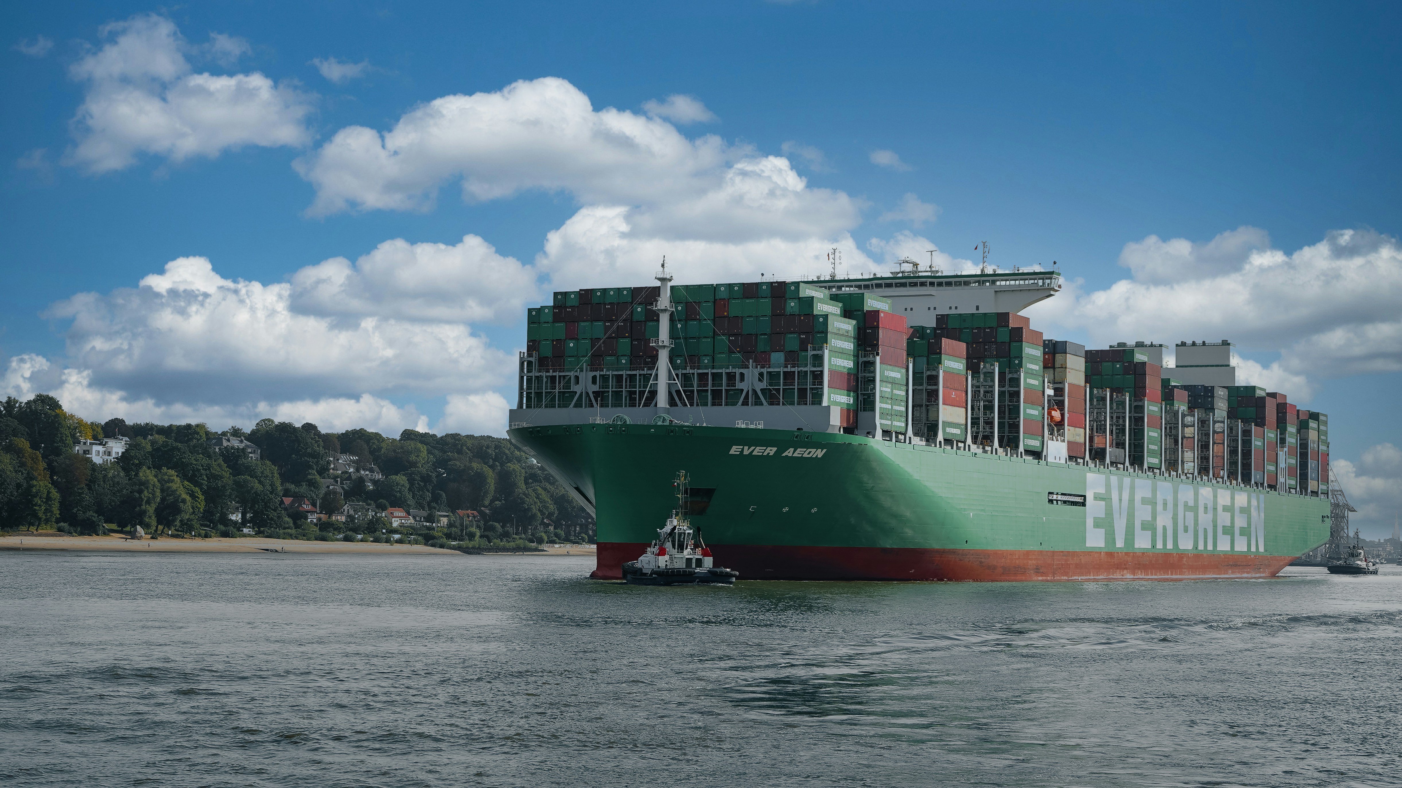Green Giant on the River: A Containership Gliding Past Shoreline