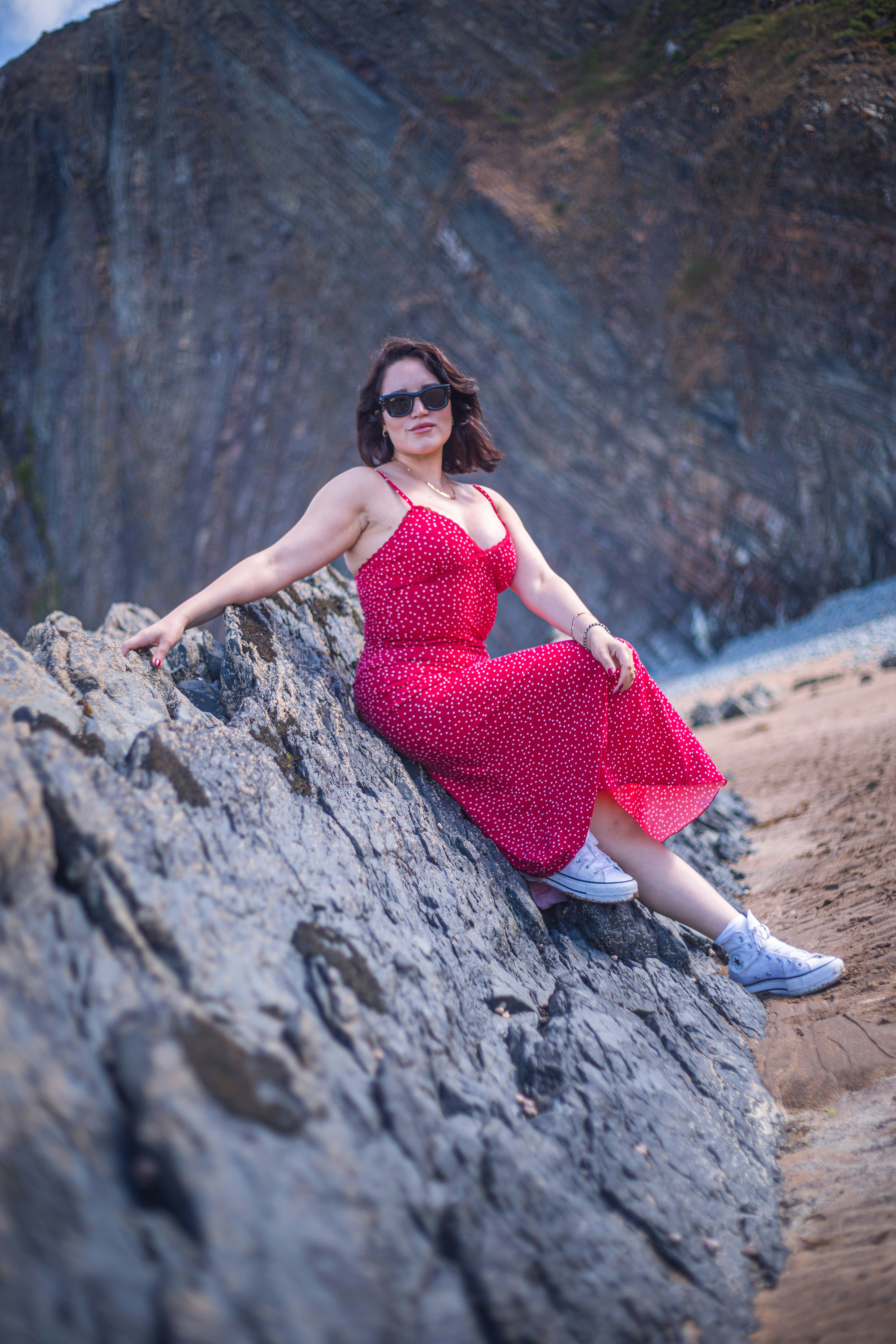 Red dress on the rugged shore: a poised moment against layered cliff backdrops