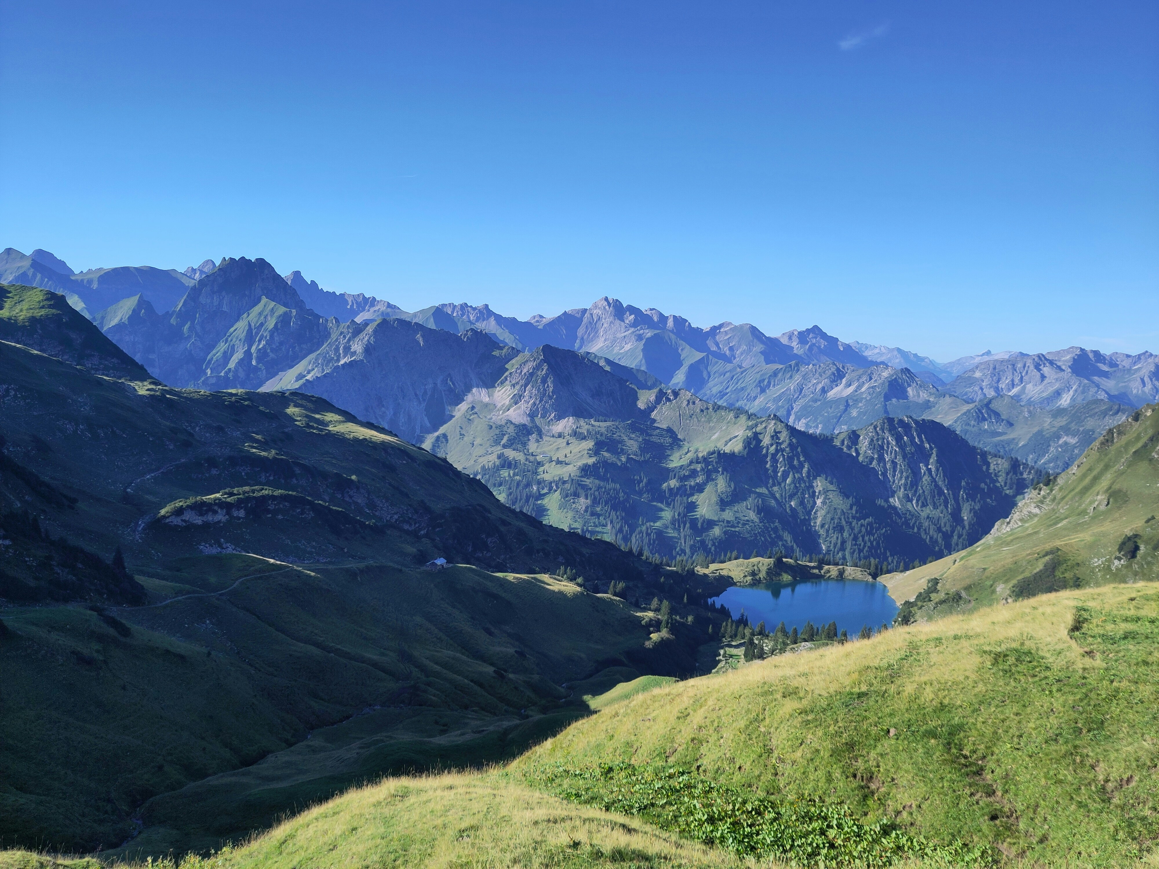Rolling green slopes cradle a tranquil alpine lake beneath jagged peaks, revealing a pristine highland landscape.