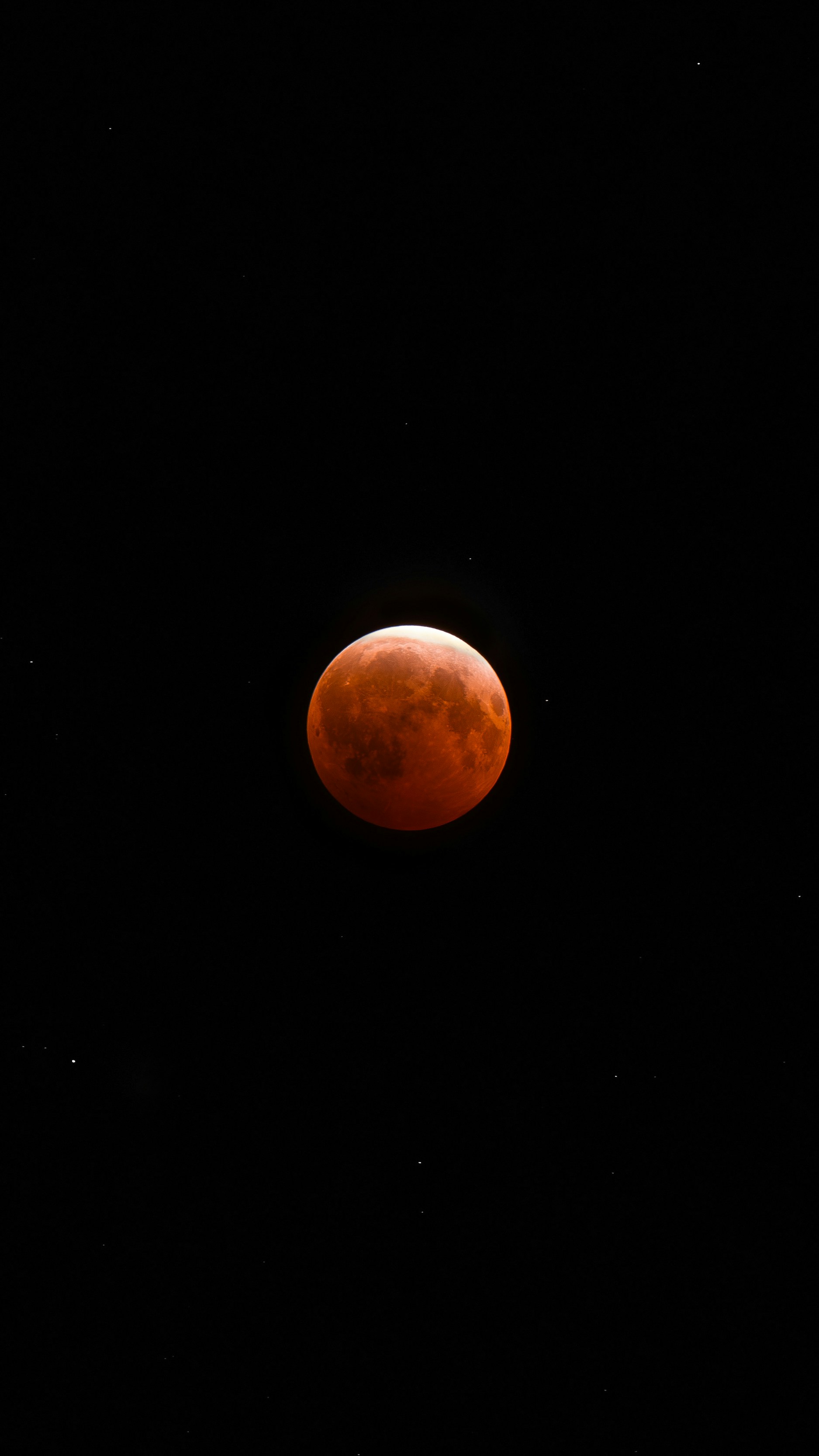 Dark night sky with a prominent reddish lunar eclipse in the center, surrounded by scattered stars.