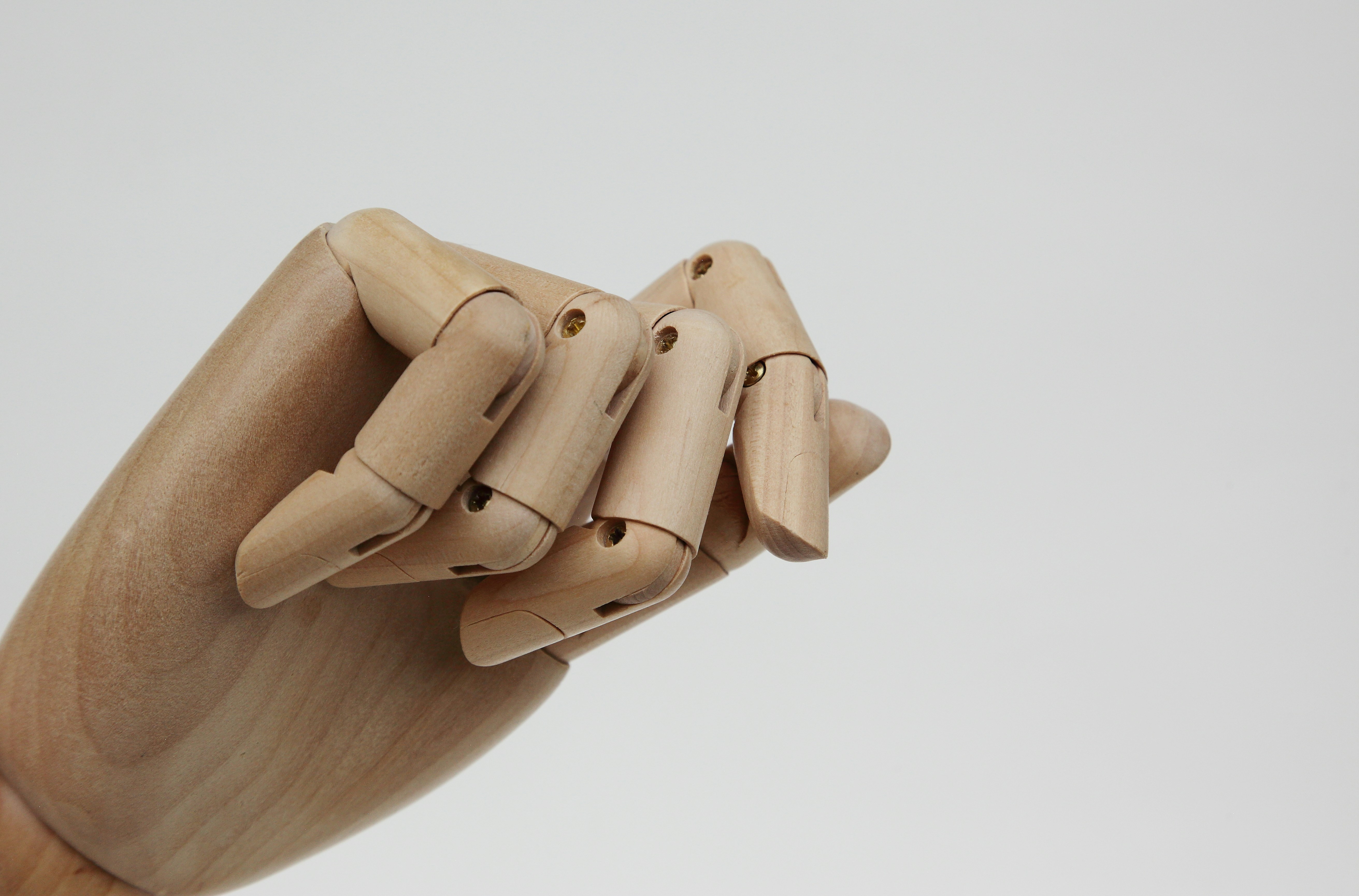 Wooden articulated hand sculpture posed against a pale background, highlighting craftsmanship and joints.