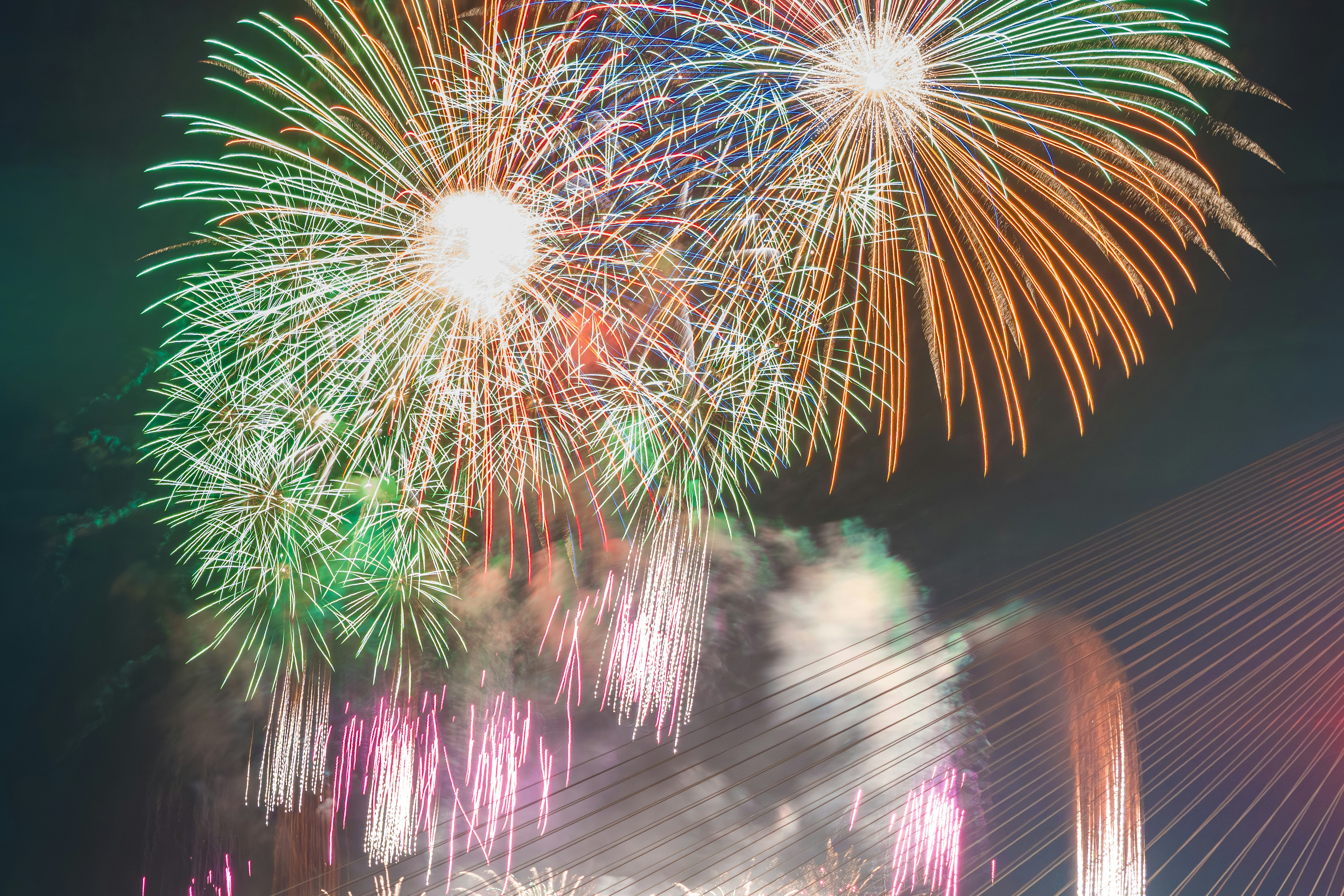 Colorful fireworks exploding in the night sky above a cable-stayed bridge