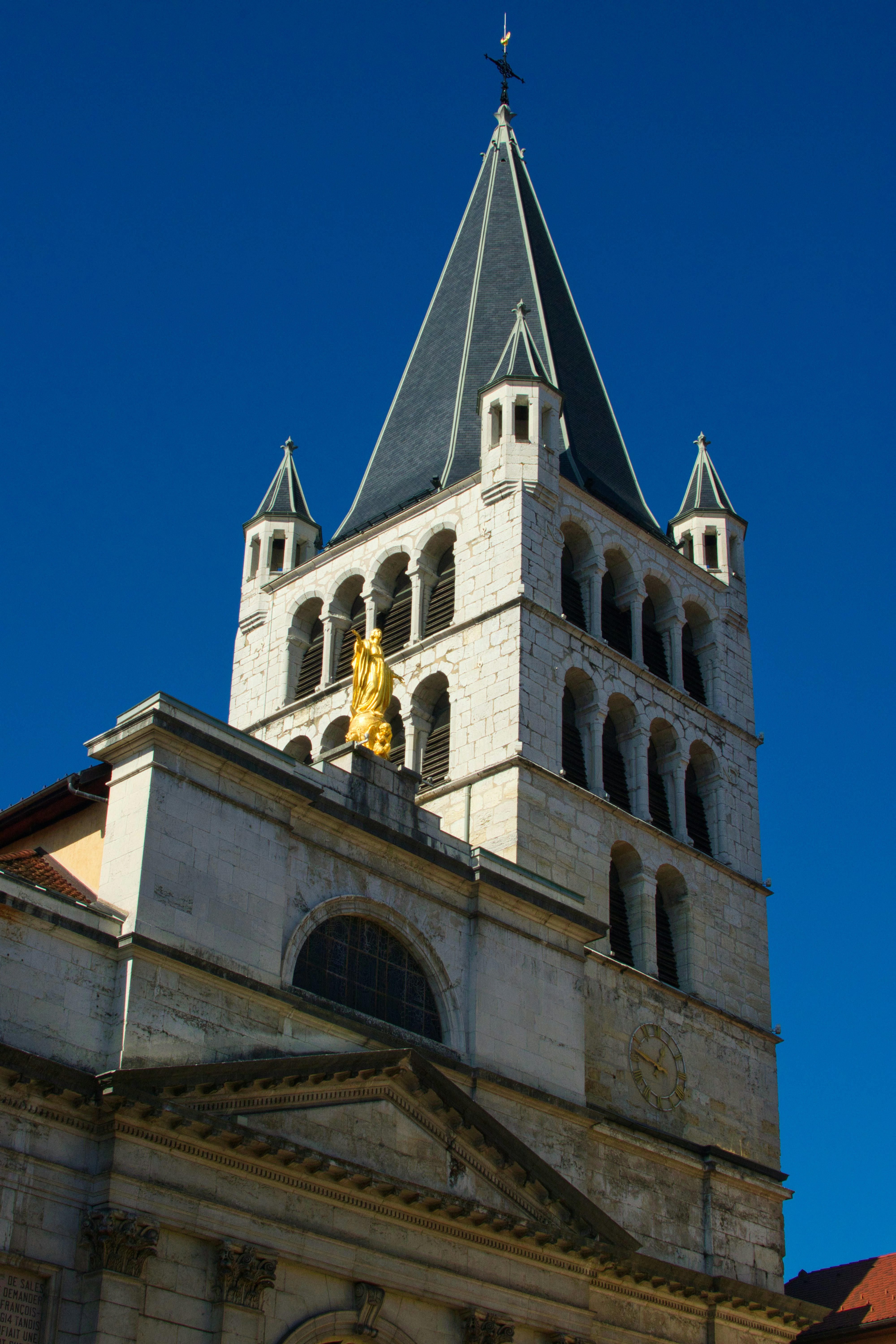 Golden Statue Beside a Stone Cathedral Spire under a Clear Blue Sky