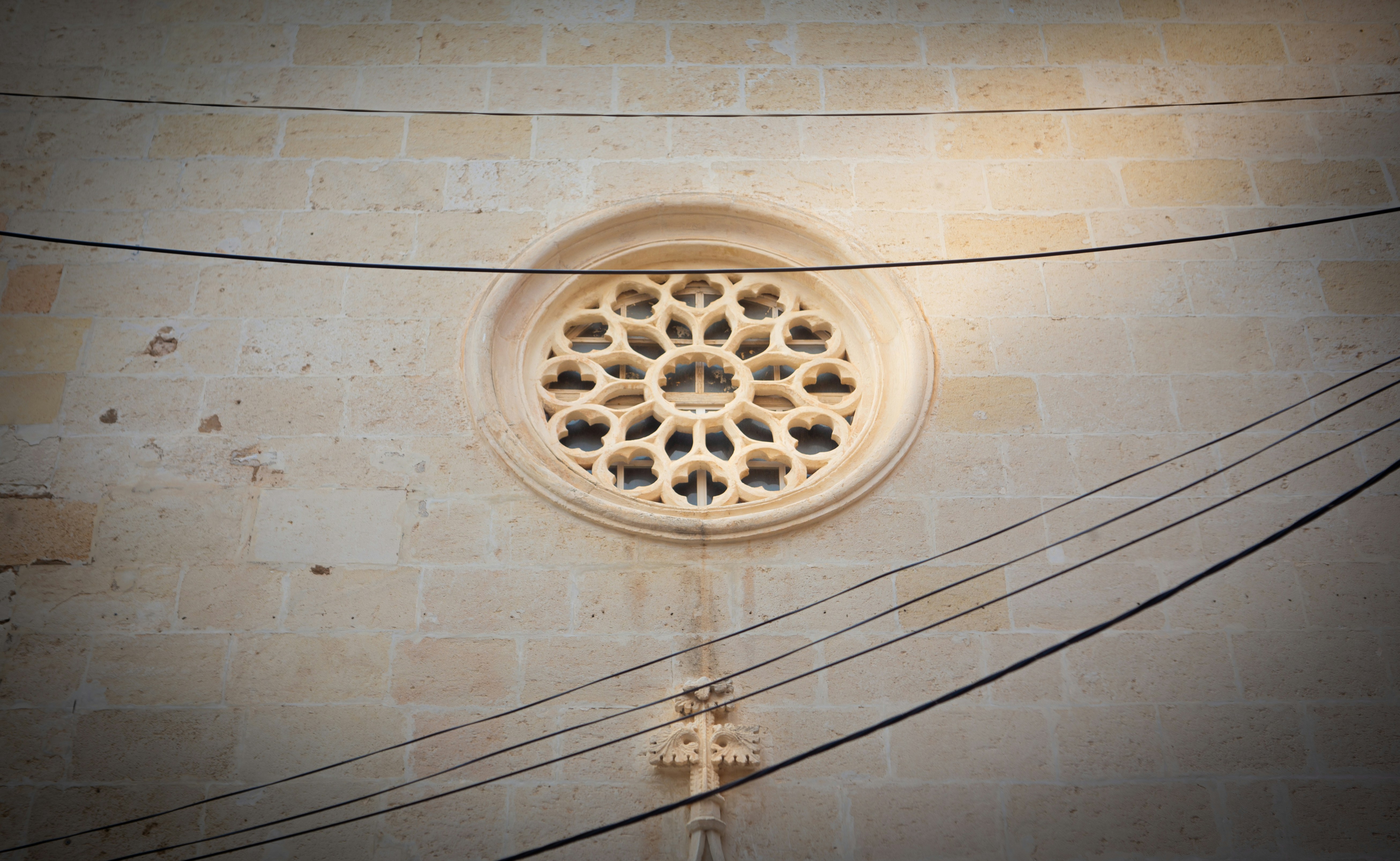 Circular carved window on sun-baked stone façade with overhead wires