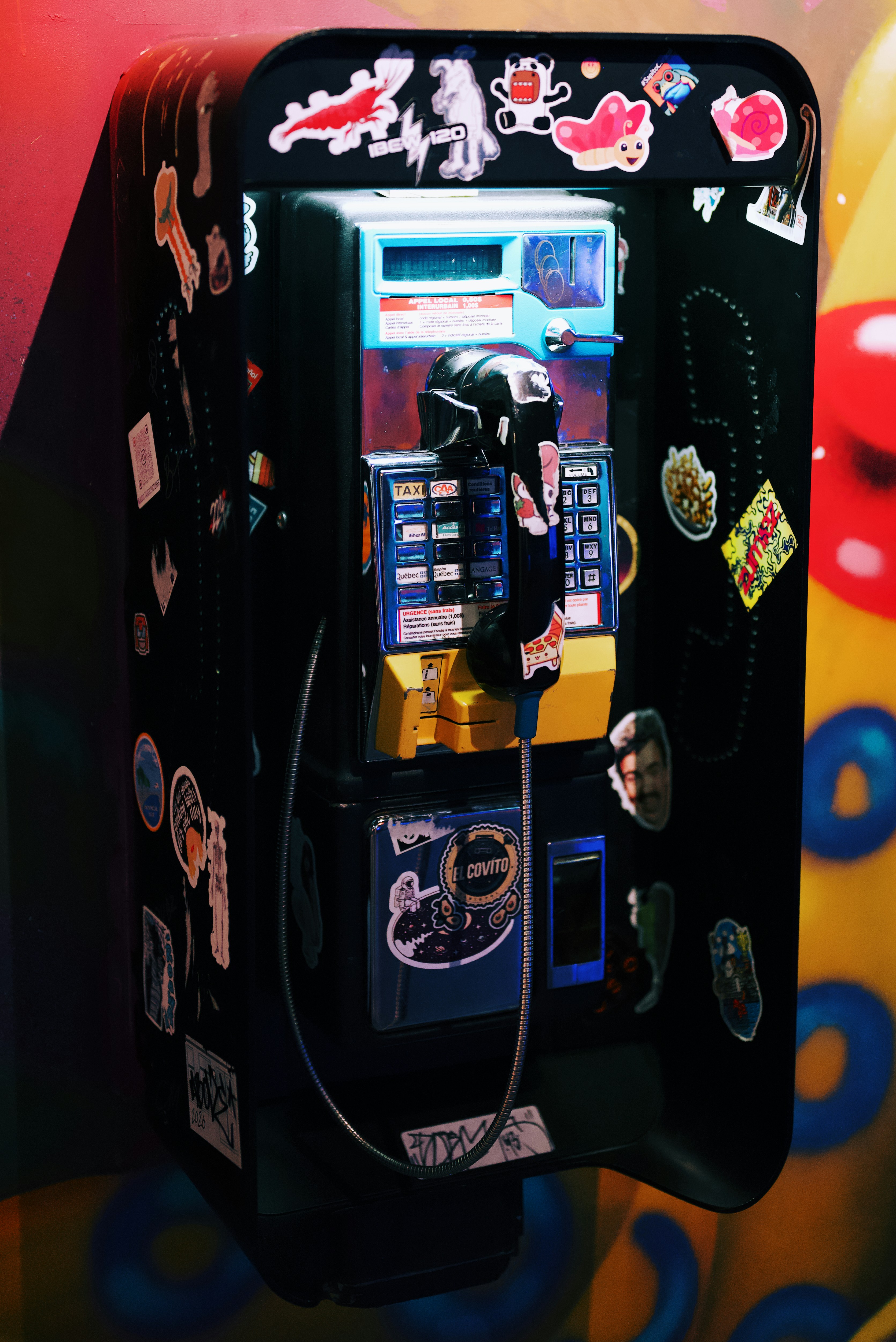 Streetside Silence: A Stickered Payphone in Neon Playground