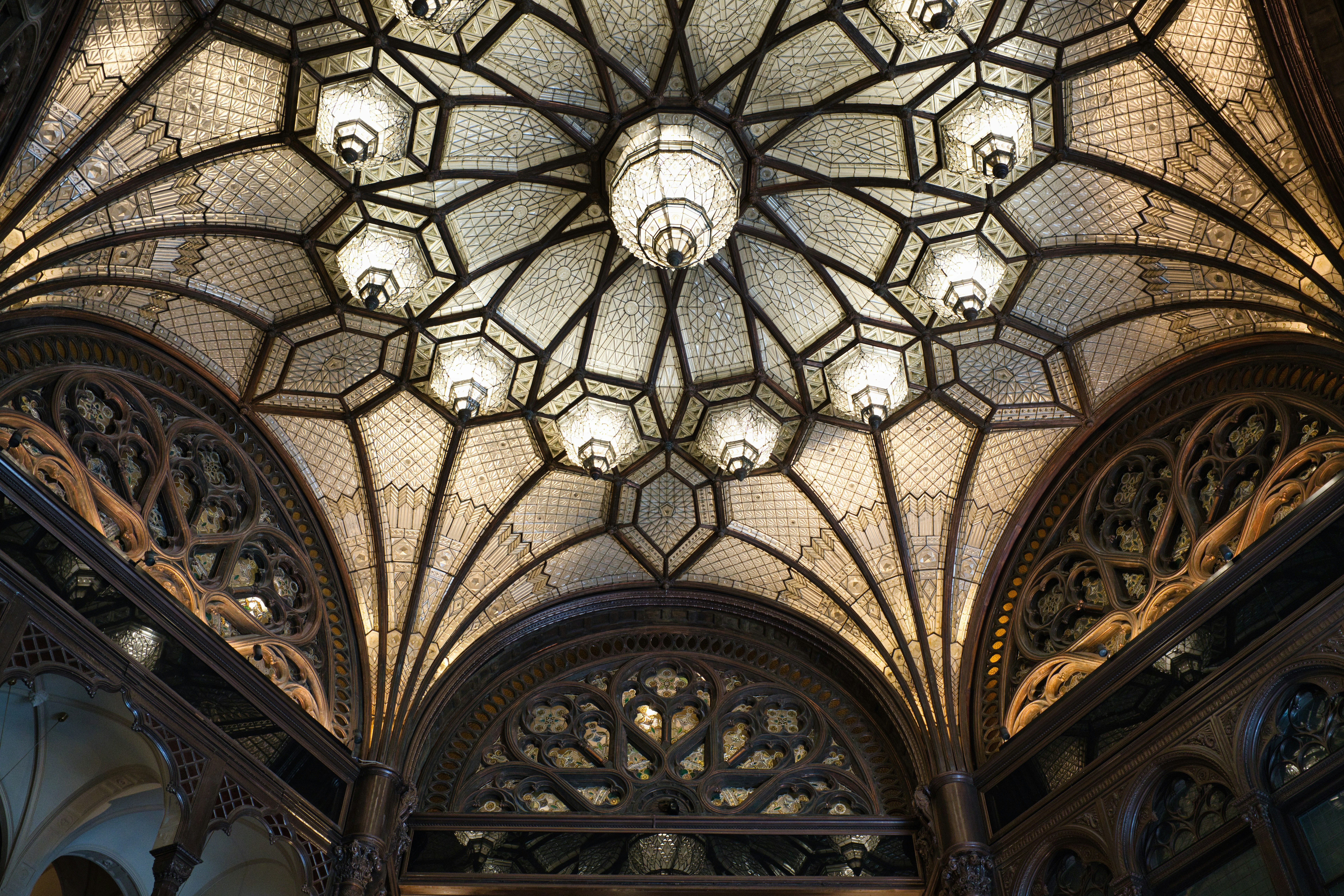 An ornate vaulted ceiling with stained glass panels and hanging pendant lights