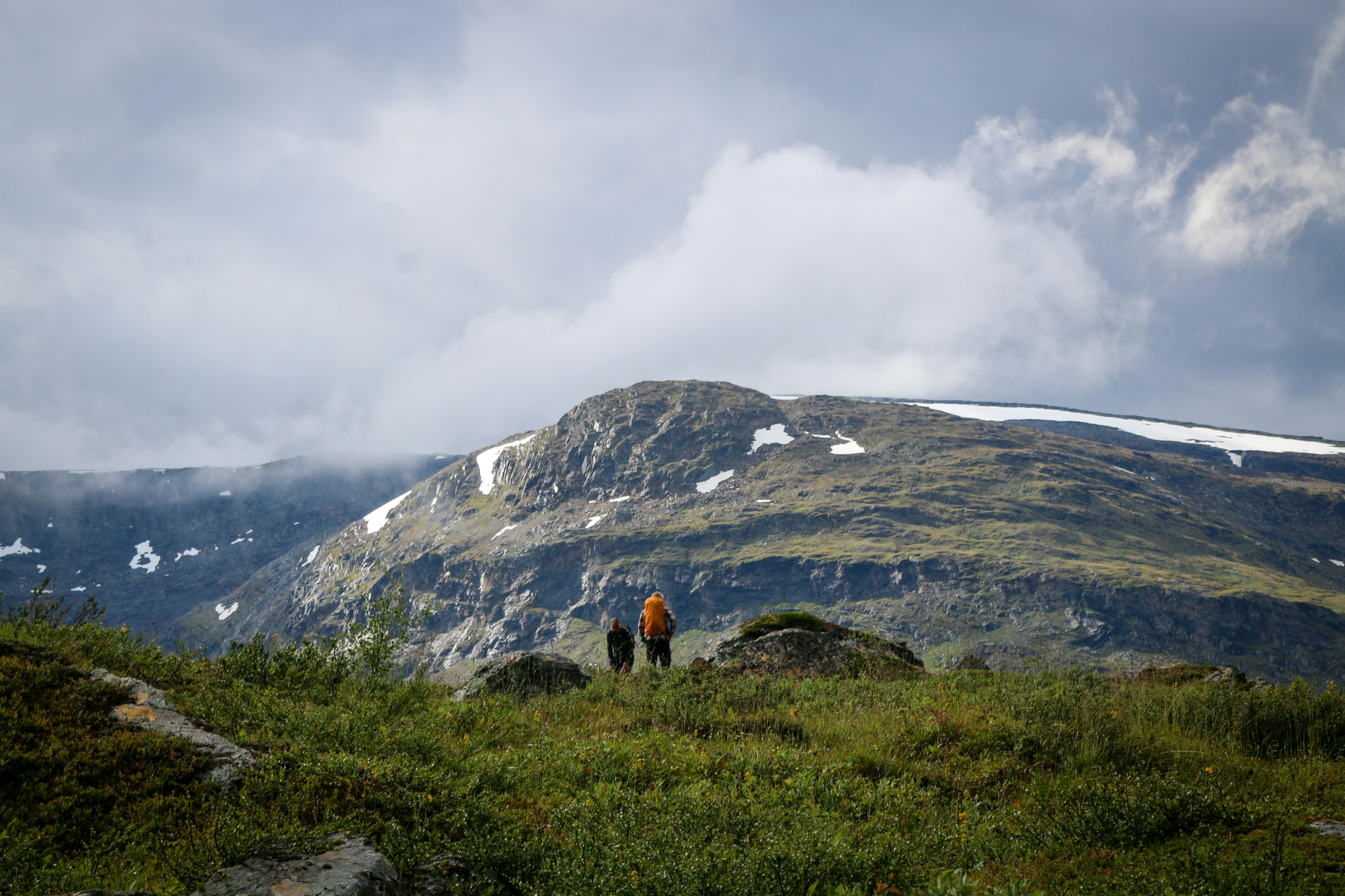 Two hikers on a windswept alpine ridge under a brooding sky
