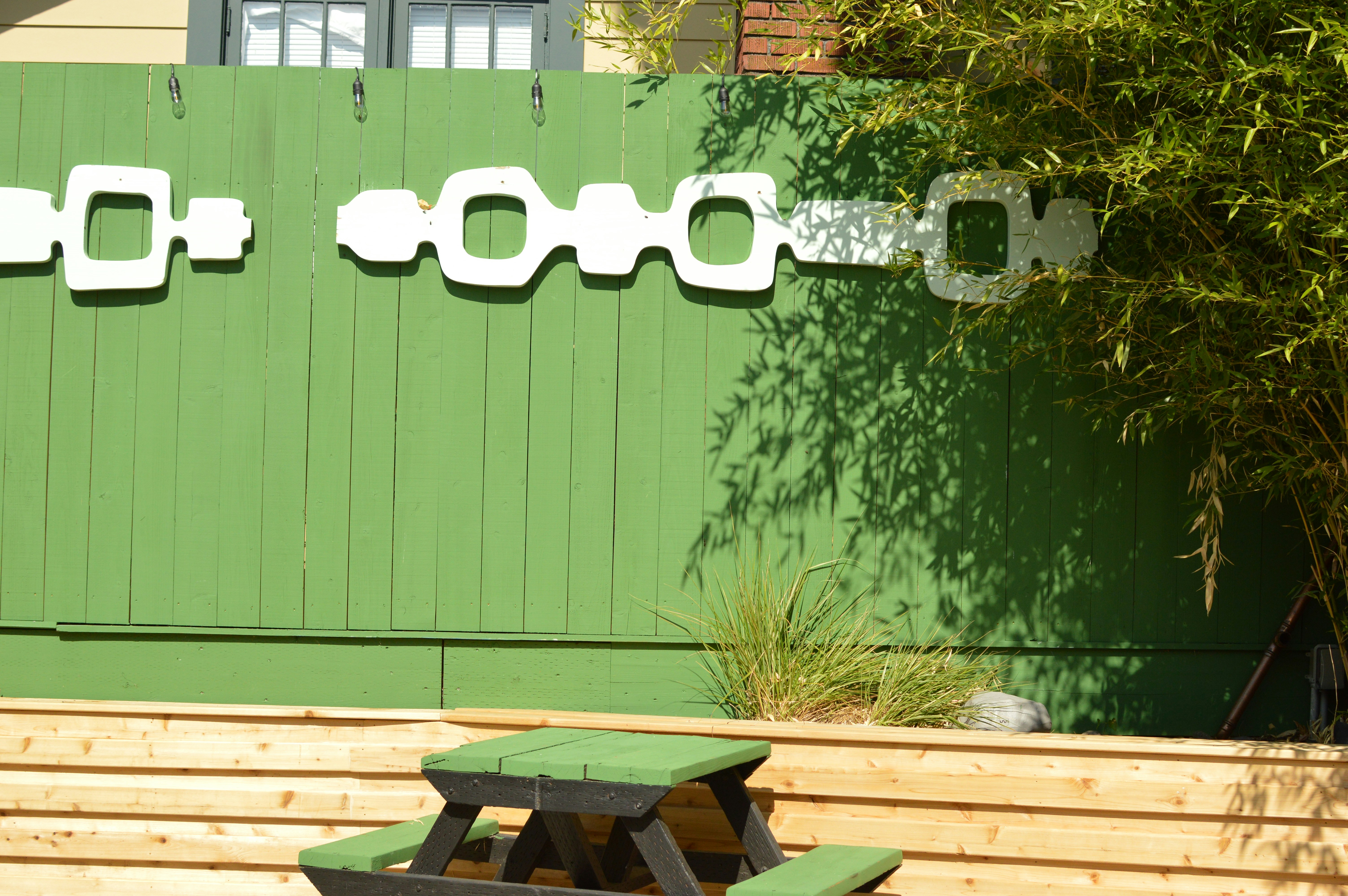 Green Wall Letters: A Bite of Outdoor Seating and Shadowed Pines