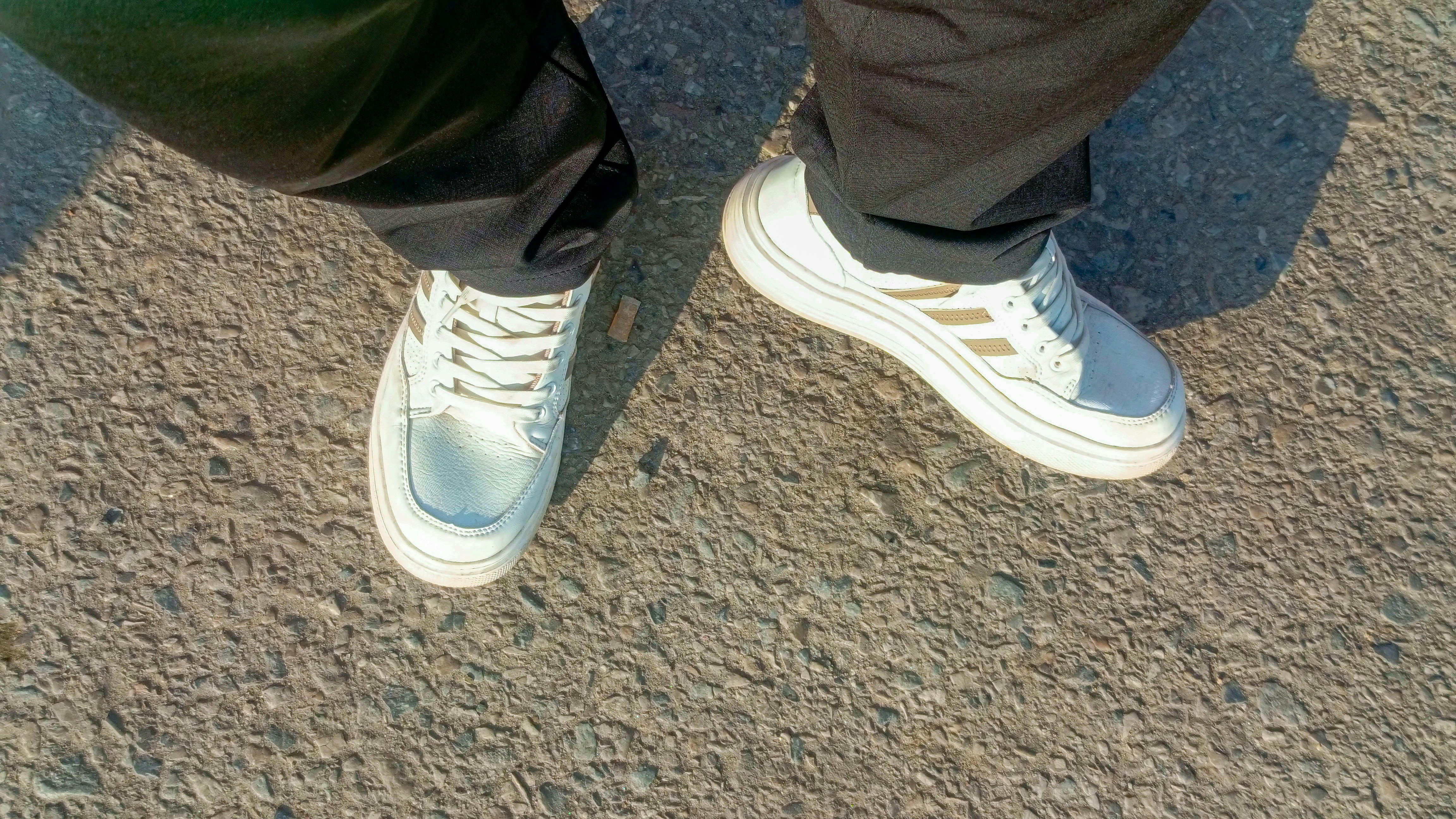 Two Sneakers Step Across a Sunlit Asphalt