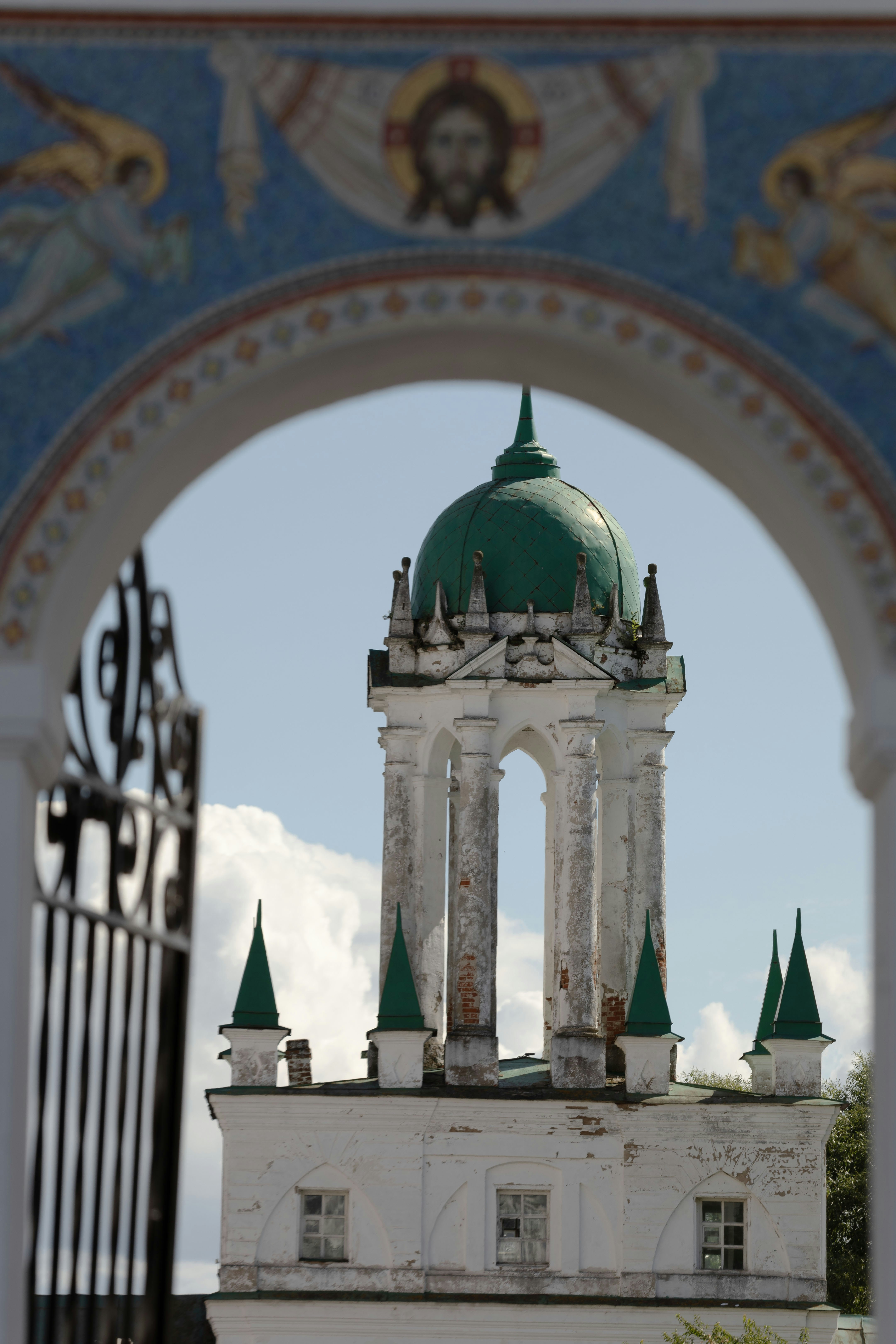 Green-domed tower crowned by weathered spires under a sacred arch