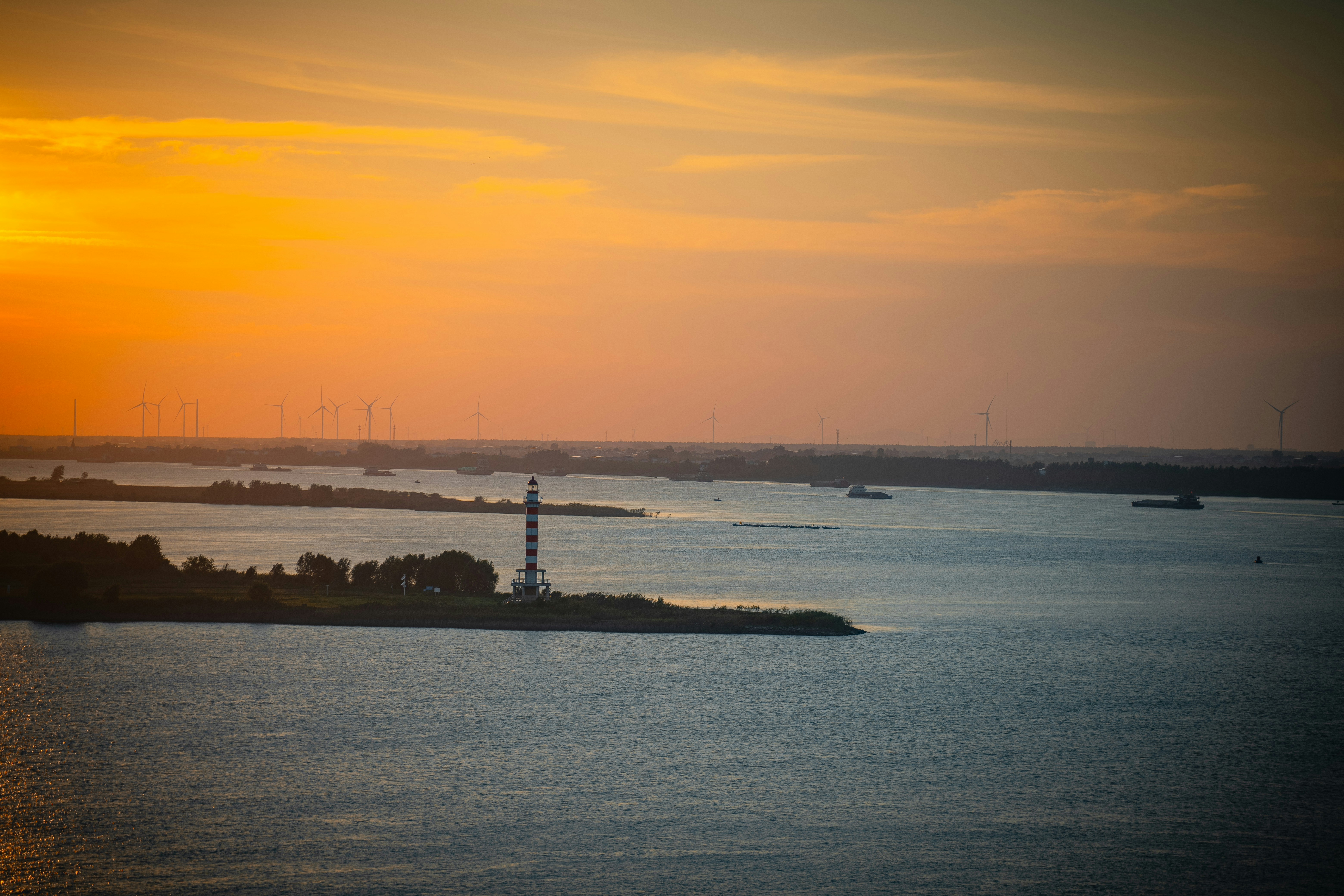 Sunset Over a Distant Lighthouse: Calm Waters and Wind Turbines on the Horizon