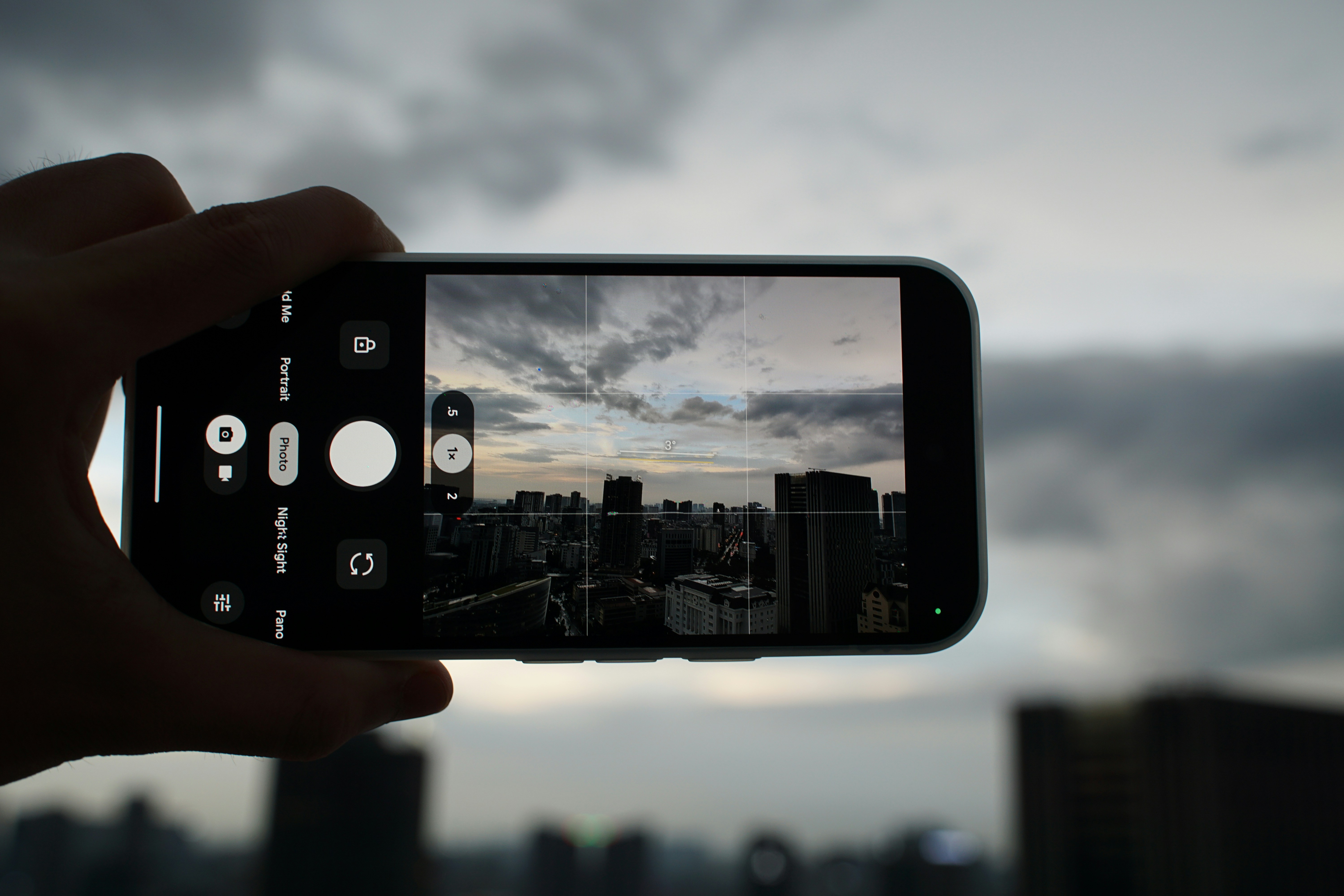 Cityscape captured through a handheld phone screen during a dim dusk