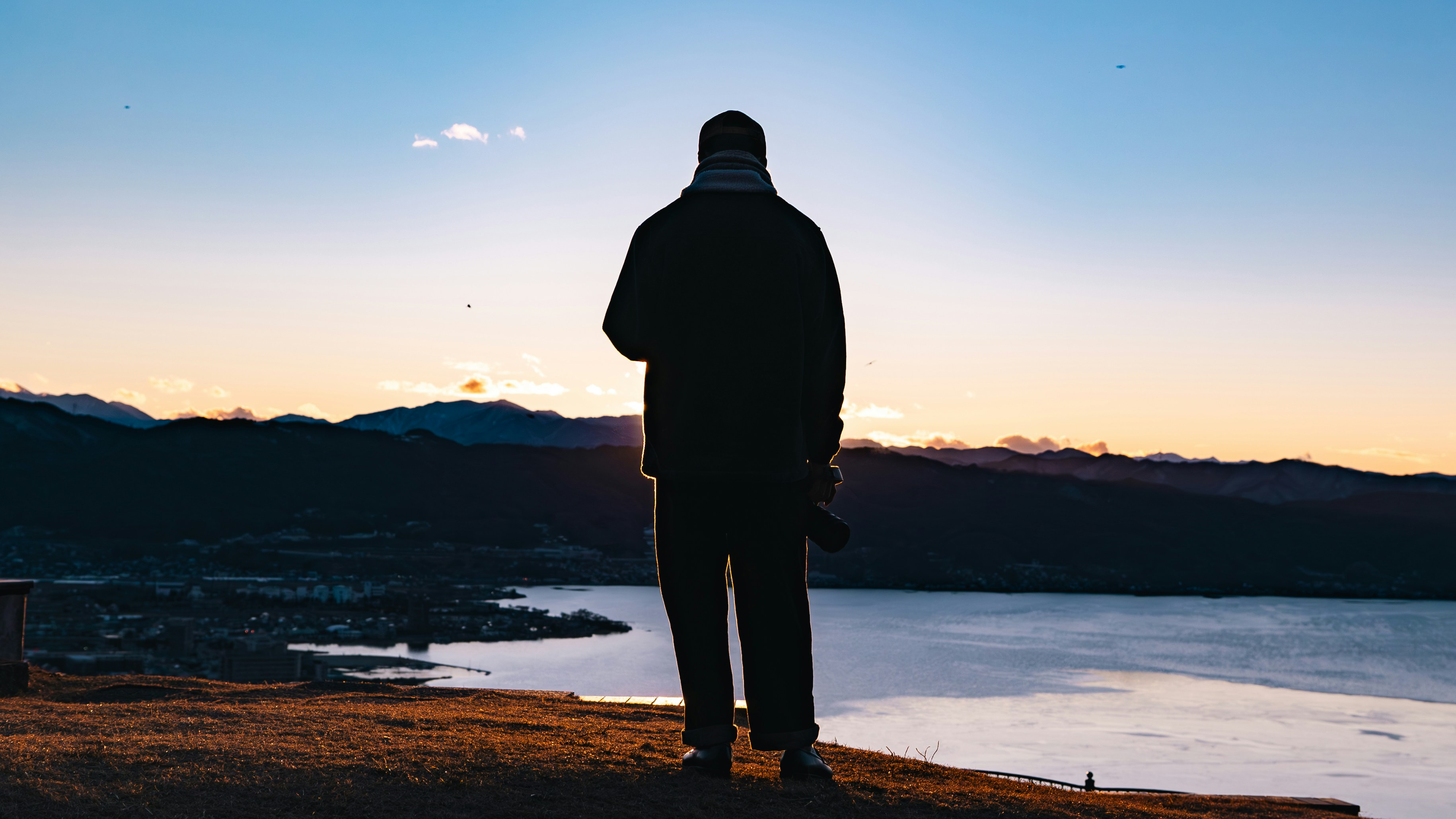 Silhouette at Dusk: A Photographer Gazes Across a Quiet Fjord