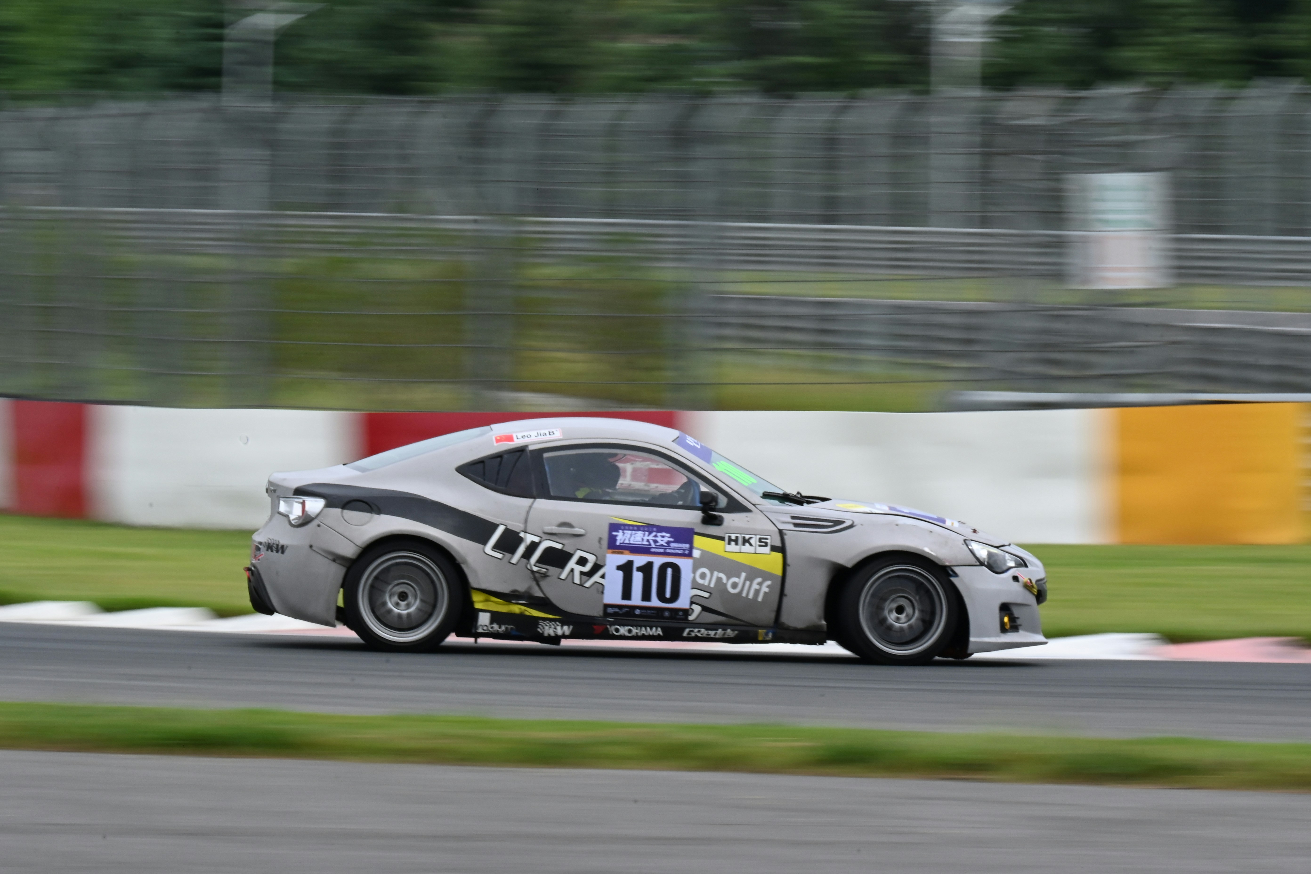 Race car speeding along a circuit with sponsor decals, captured with motion blur in the background and foreground.