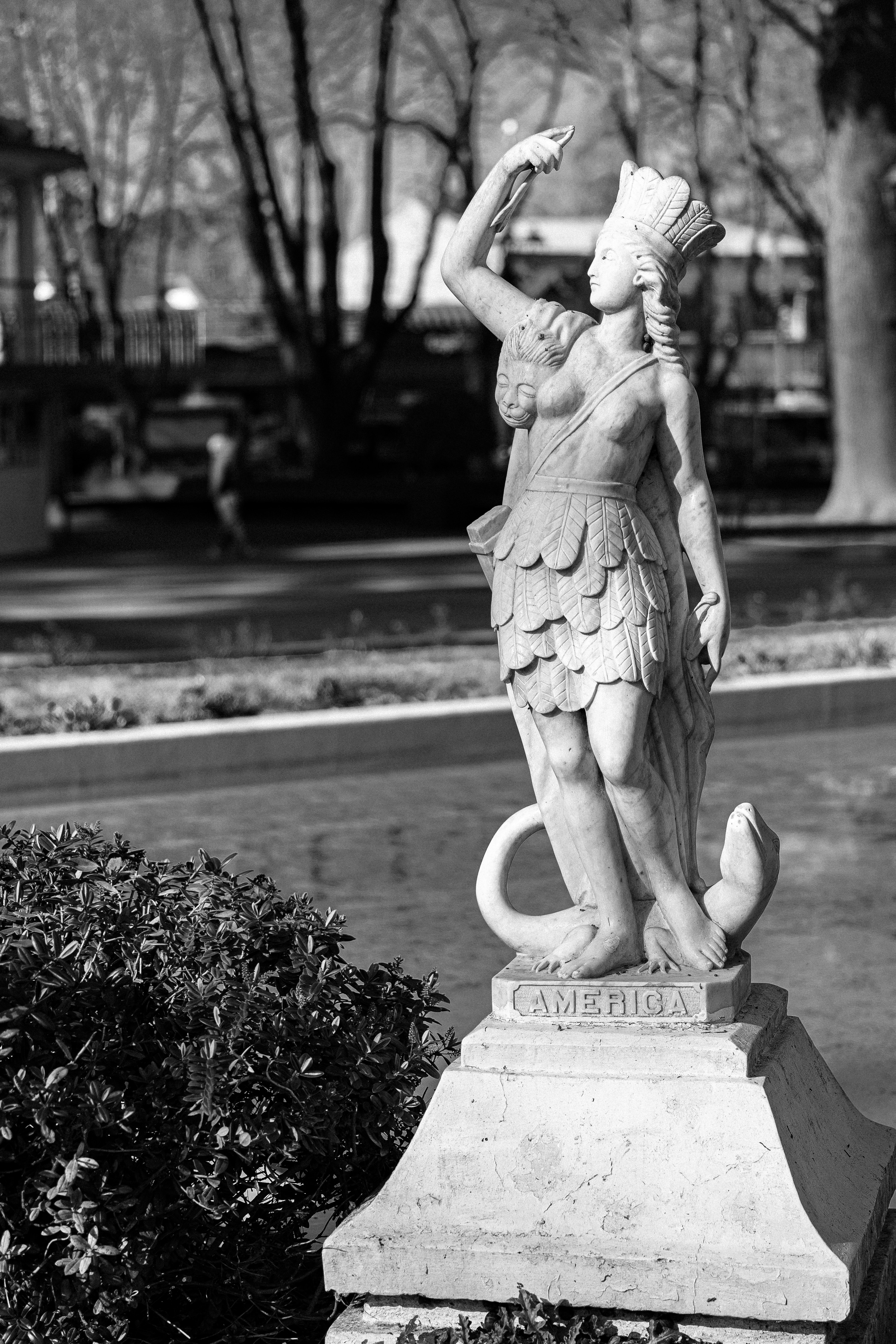 Arched Pose: a stone figure in a sunlit park fountain