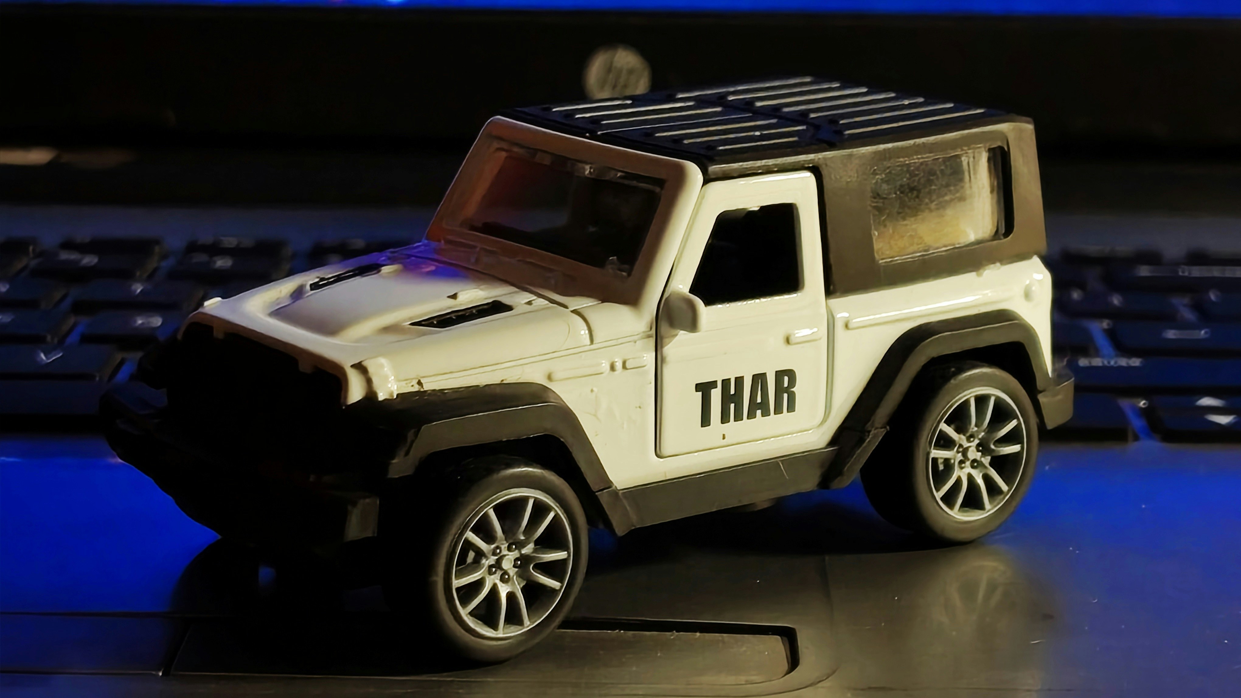 Small white THAR toy SUV sits on a laptop keyboard with blue ambient lighting in the background.