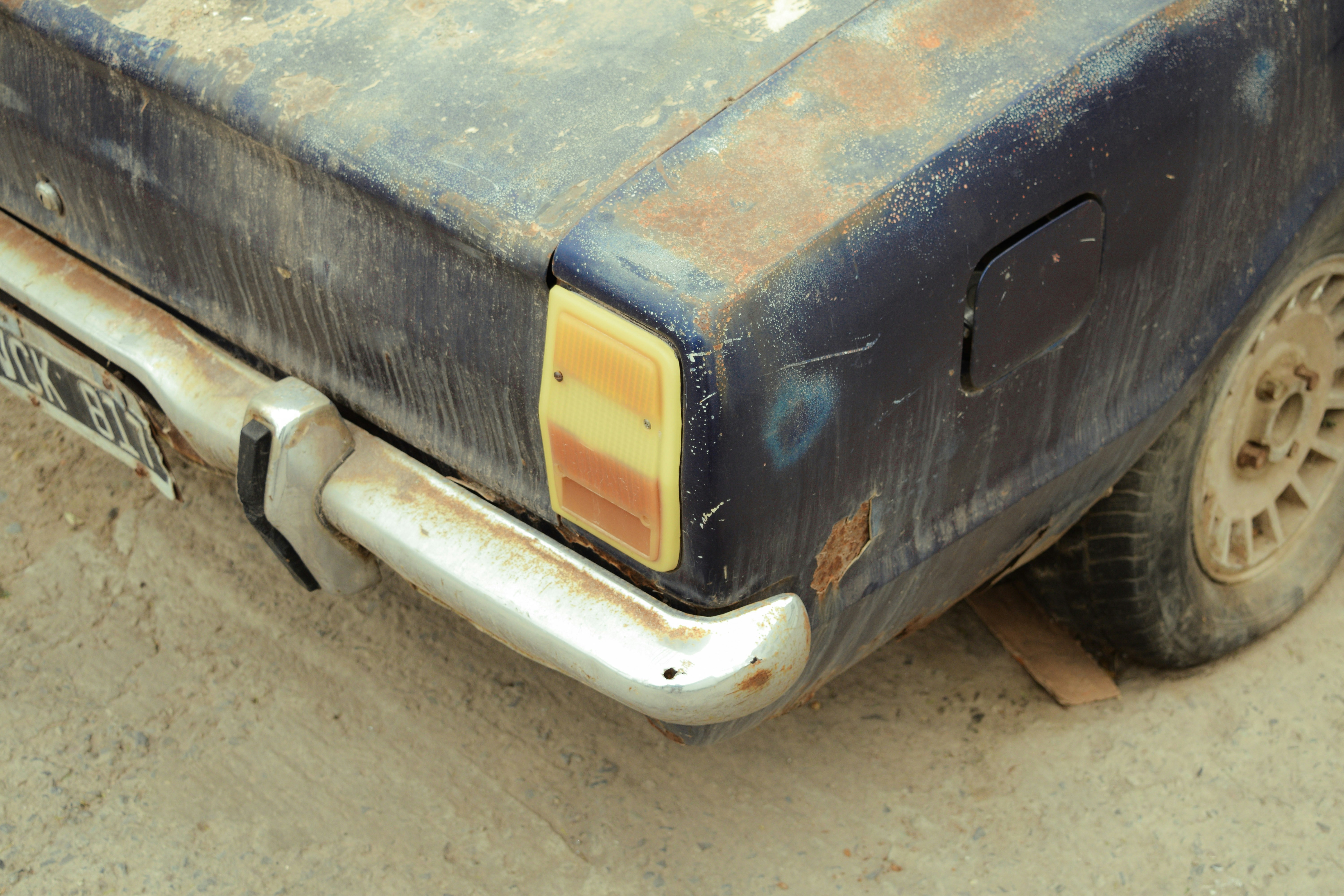 Dirt-Streaked Rear Light: A Weathered Hatchback in a Deserted Lot