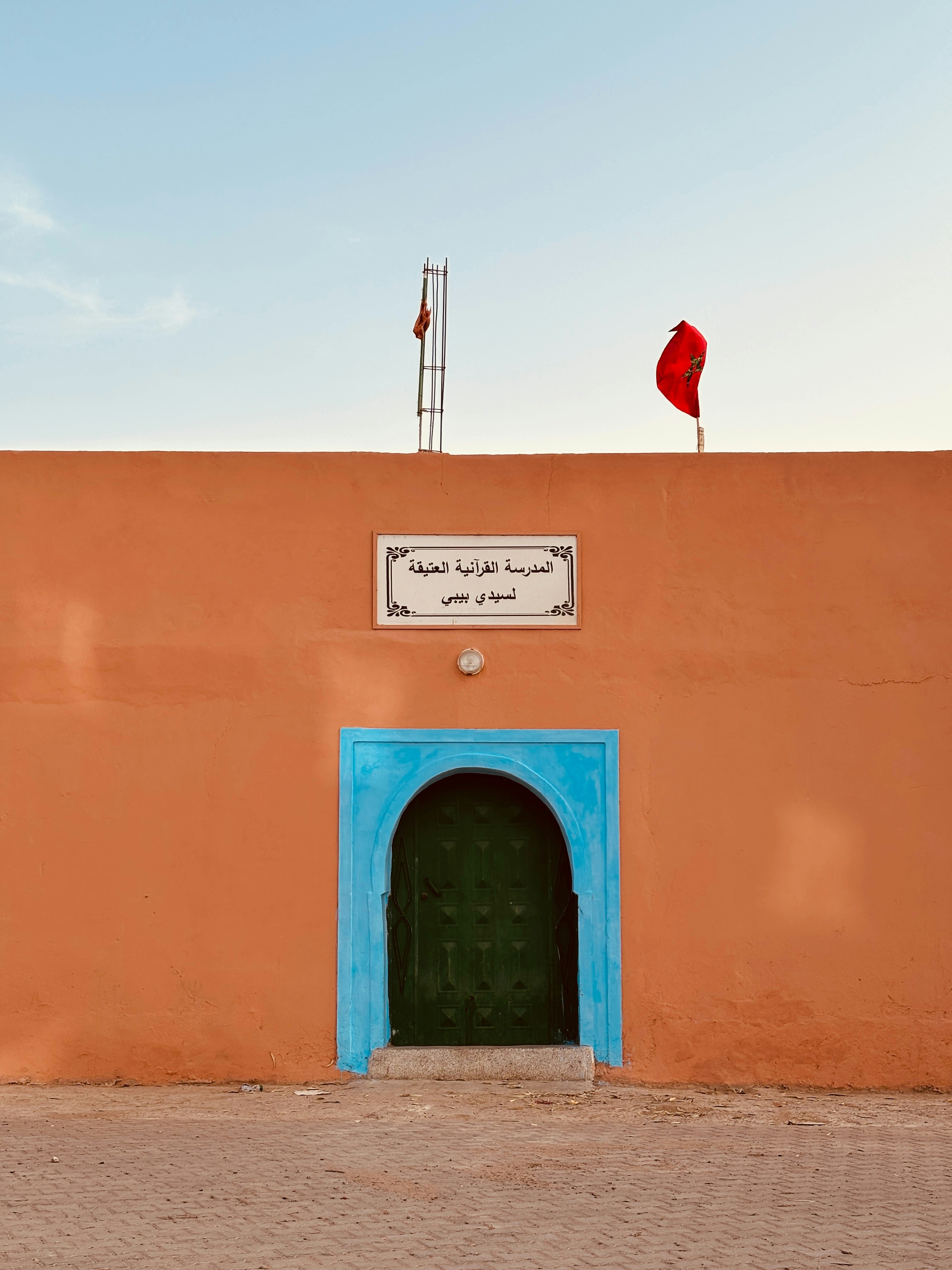Terracotta Wall, Blue Portal, and Red Flag Above a Quiet Doorway
