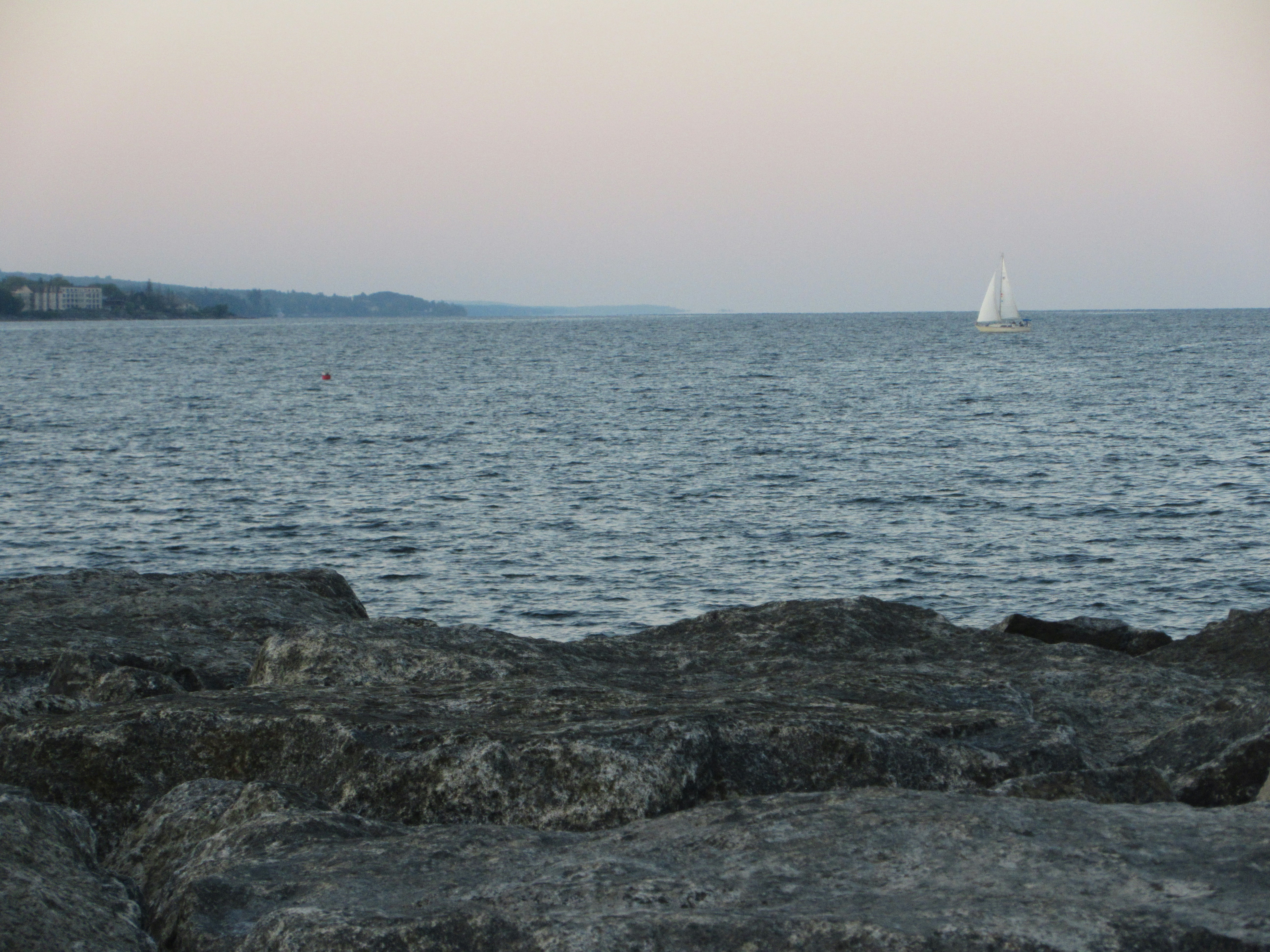 Sail on the Horizon: Quiet Sea Meets Rocky Foreground