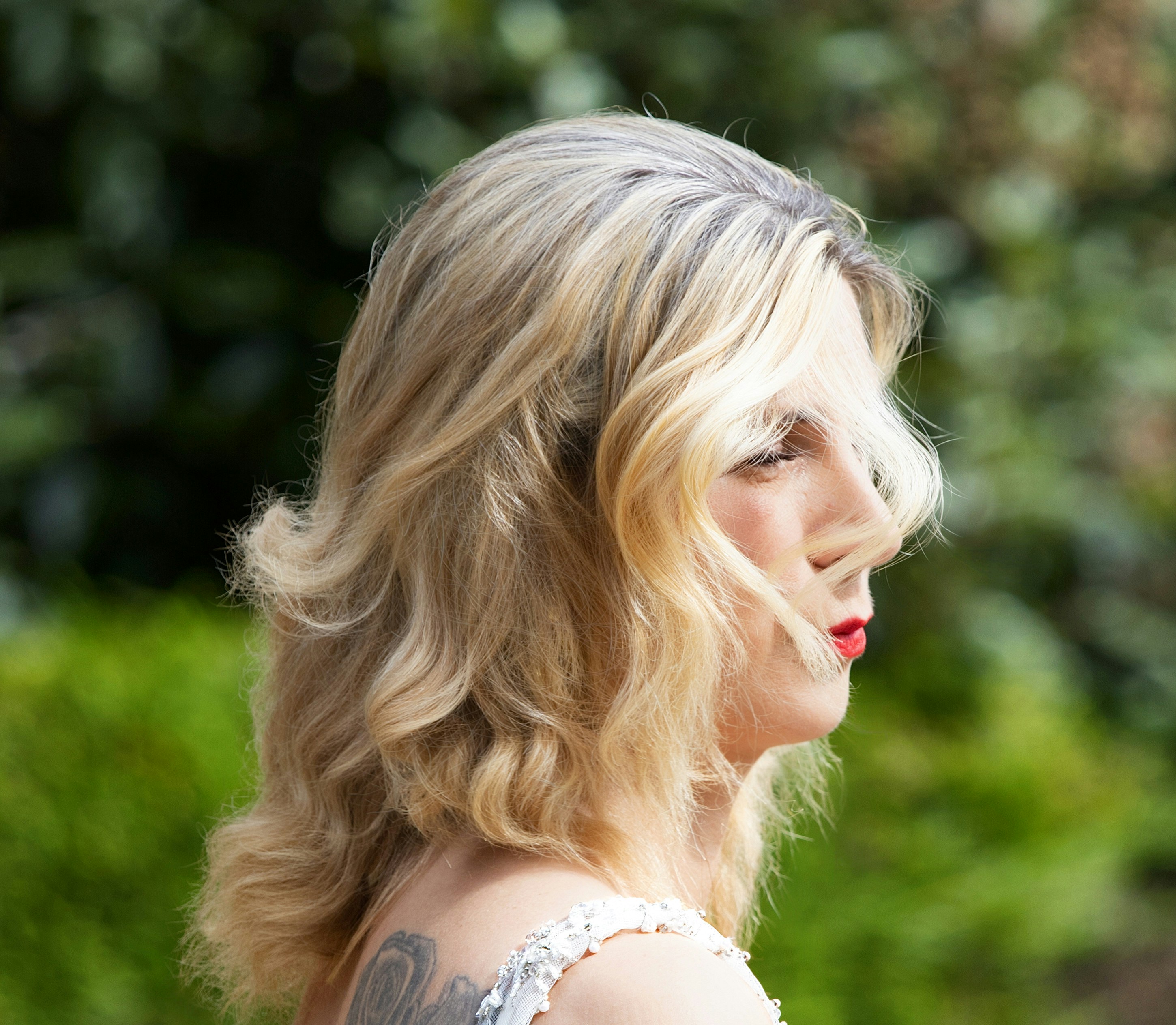 Profile view of a woman with blonde hair and a shoulder tattoo outdoors