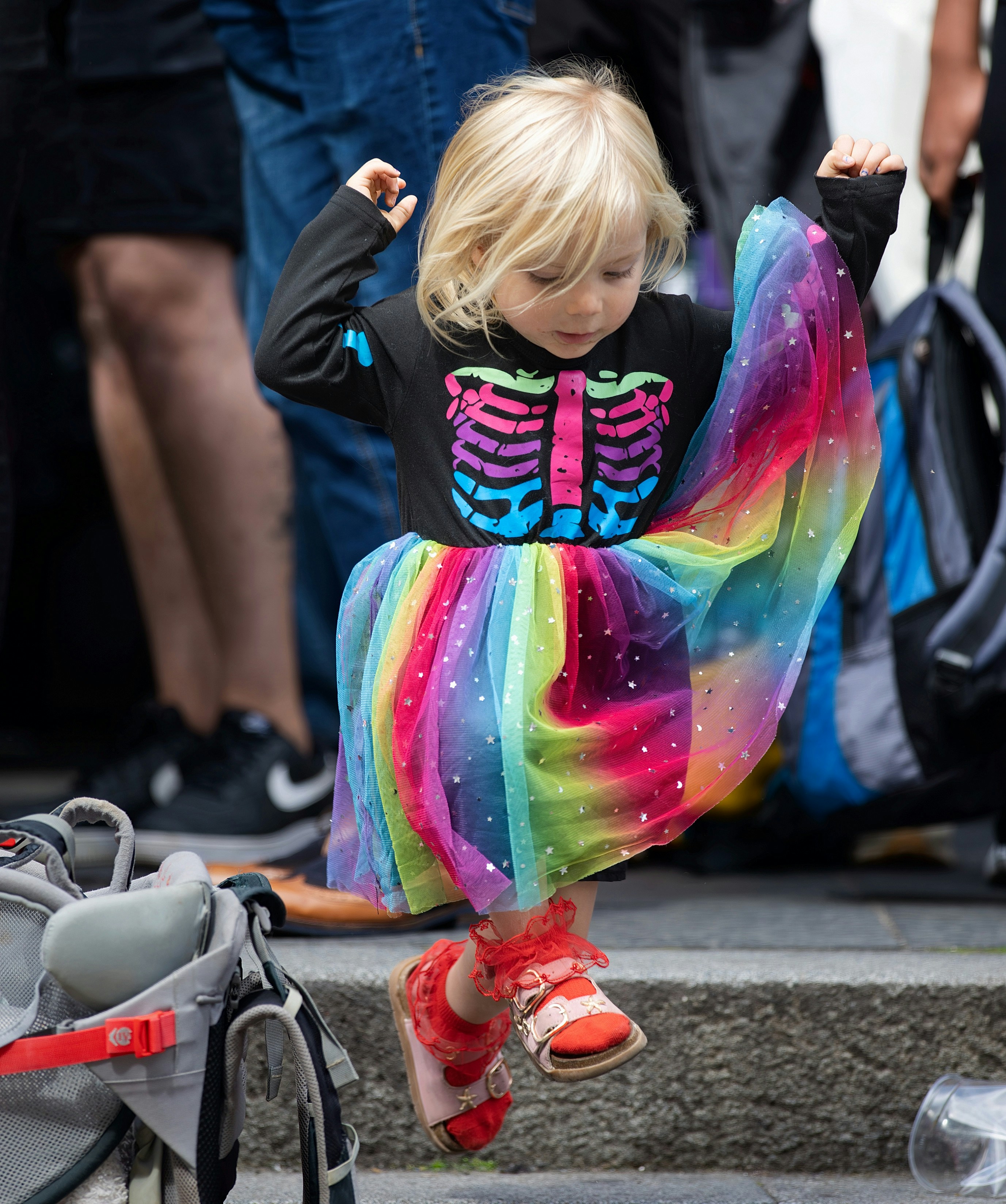 Rainbow-skirted toddler leaps amid a crowd, color and motion in bloom